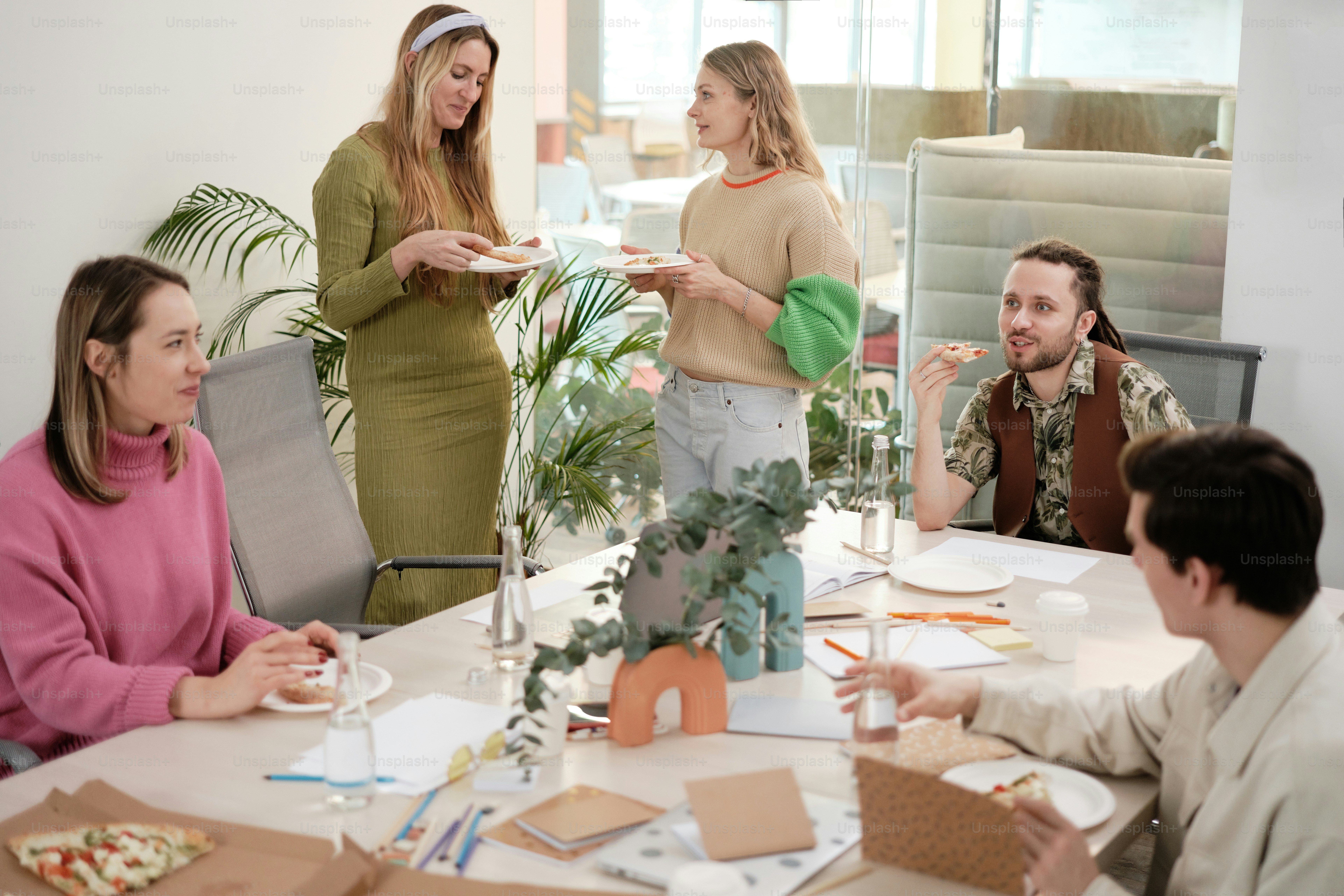 A group of people sitting around a table eating pizza photo – Meeting ...