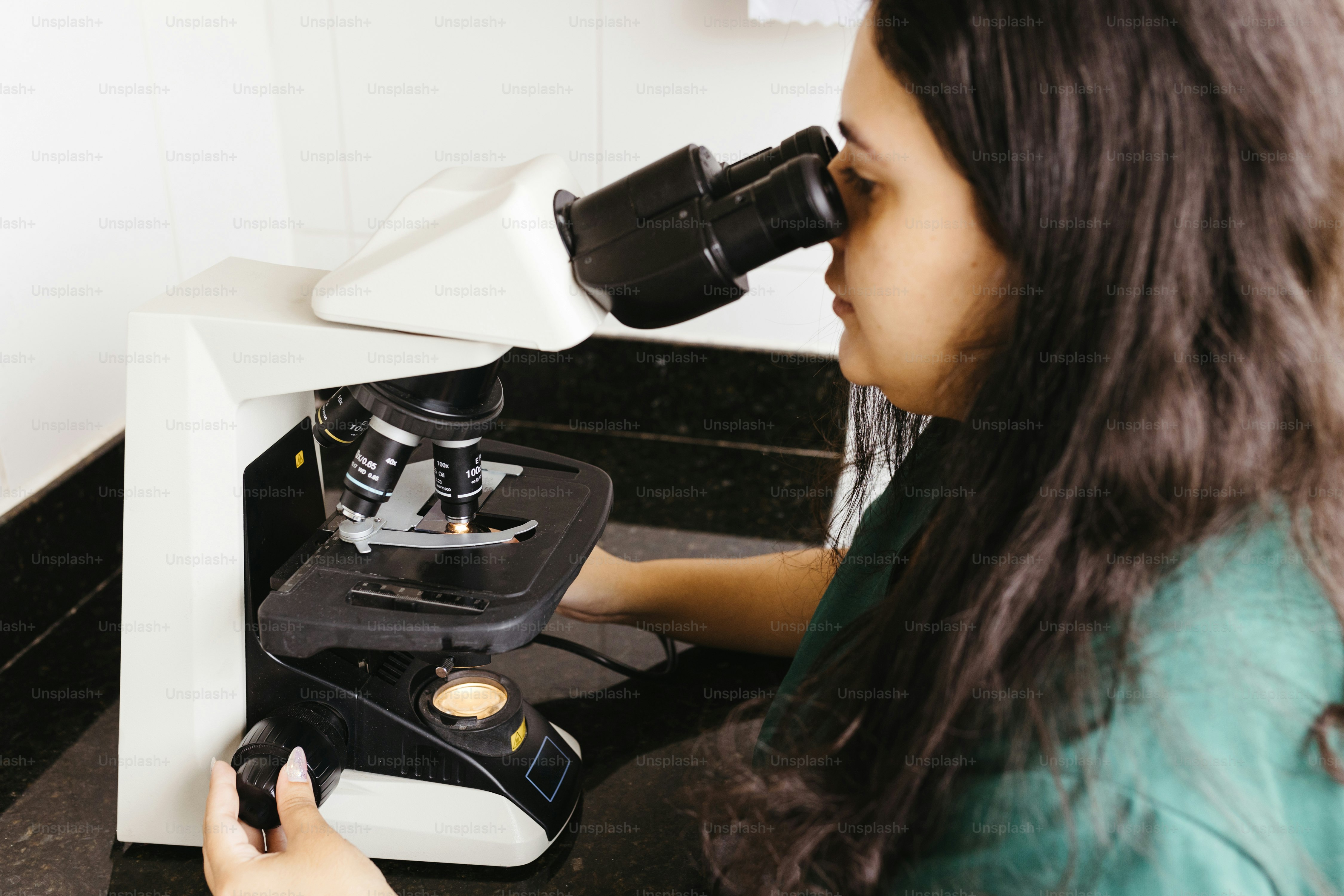 A woman looking through a microscope at something photo – Microscope ...
