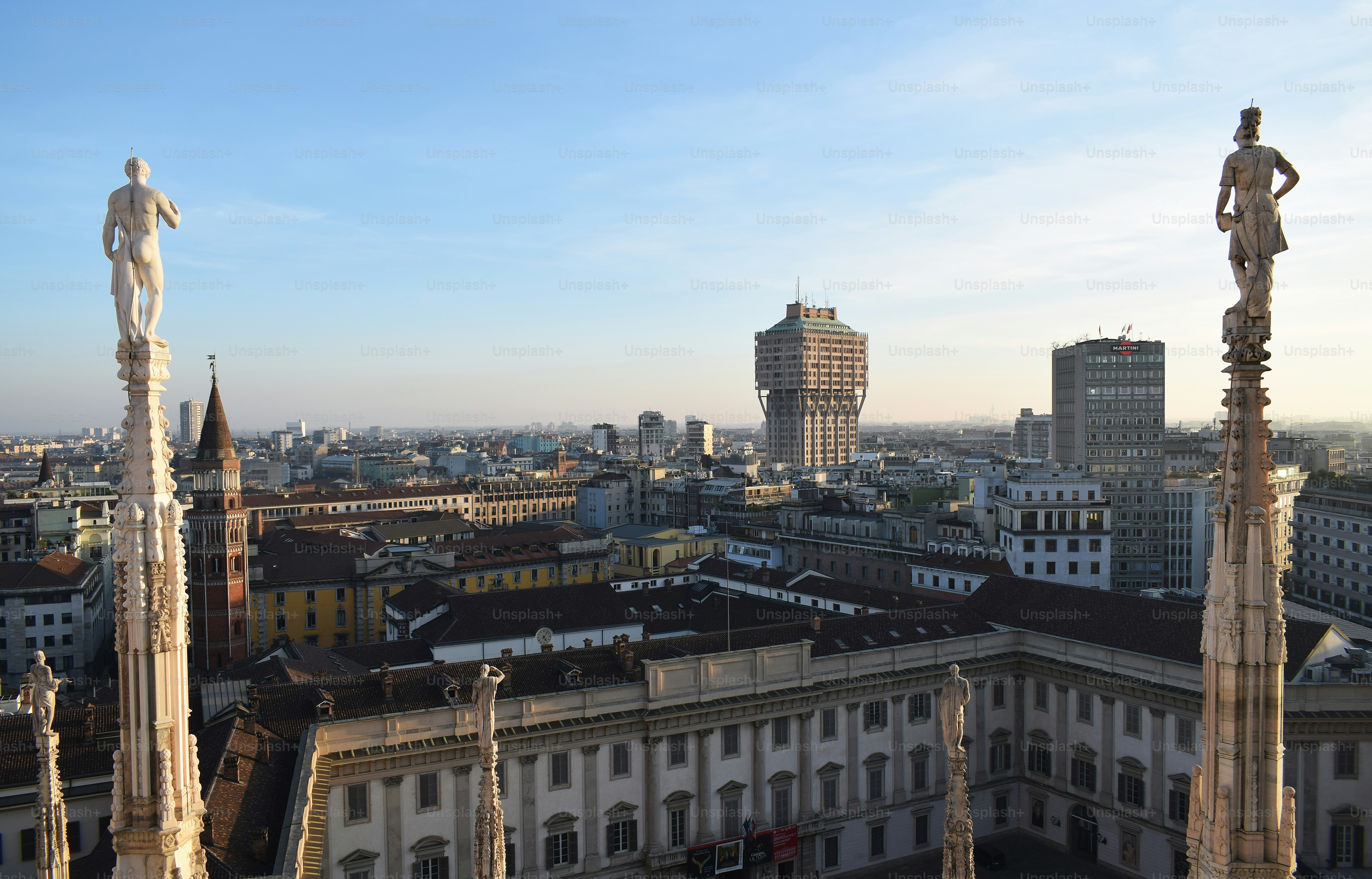 A view of a city with tall buildings and statues photo – Cityscape ...
