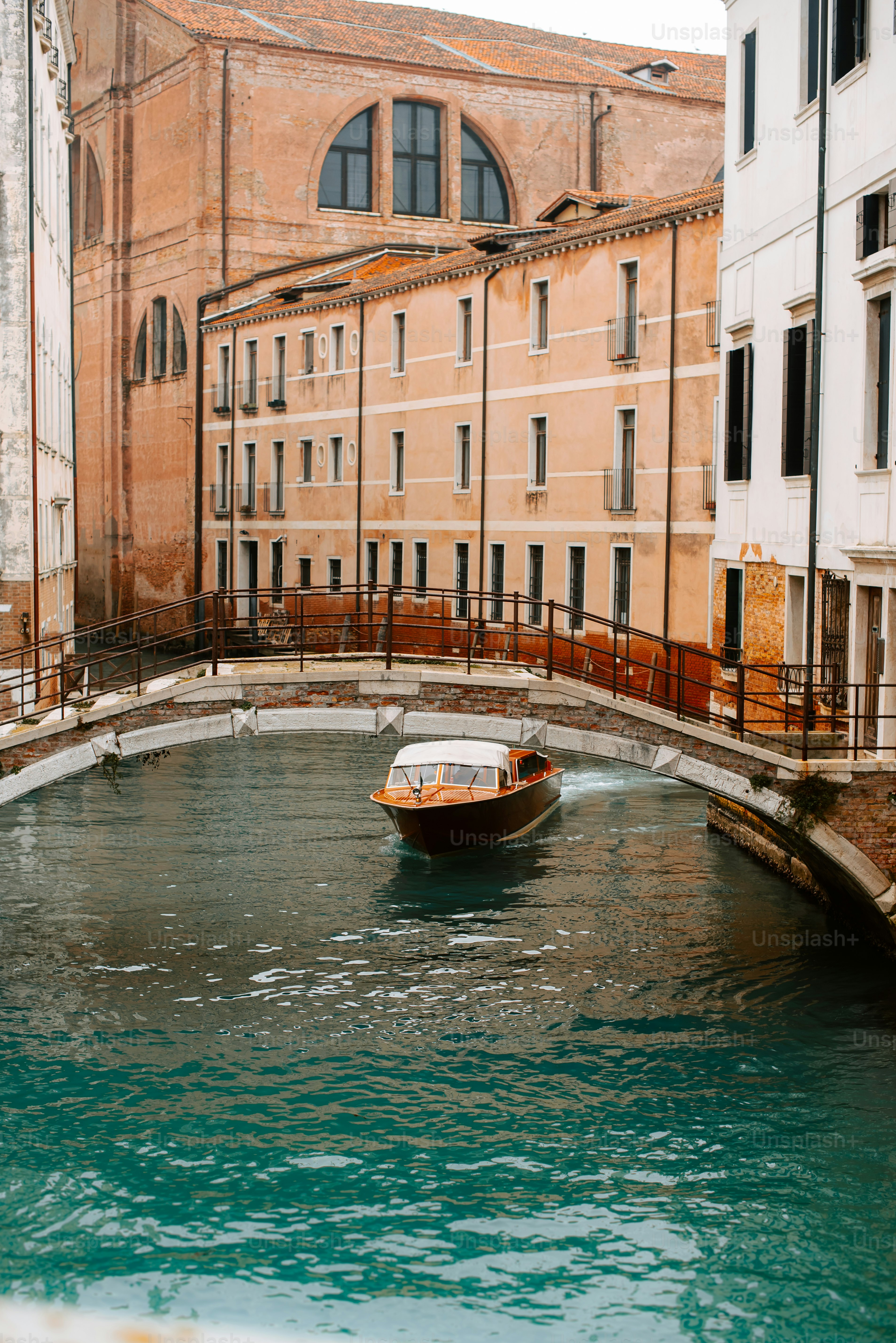 A boat traveling down a river next to tall buildings photo – Boat in ...