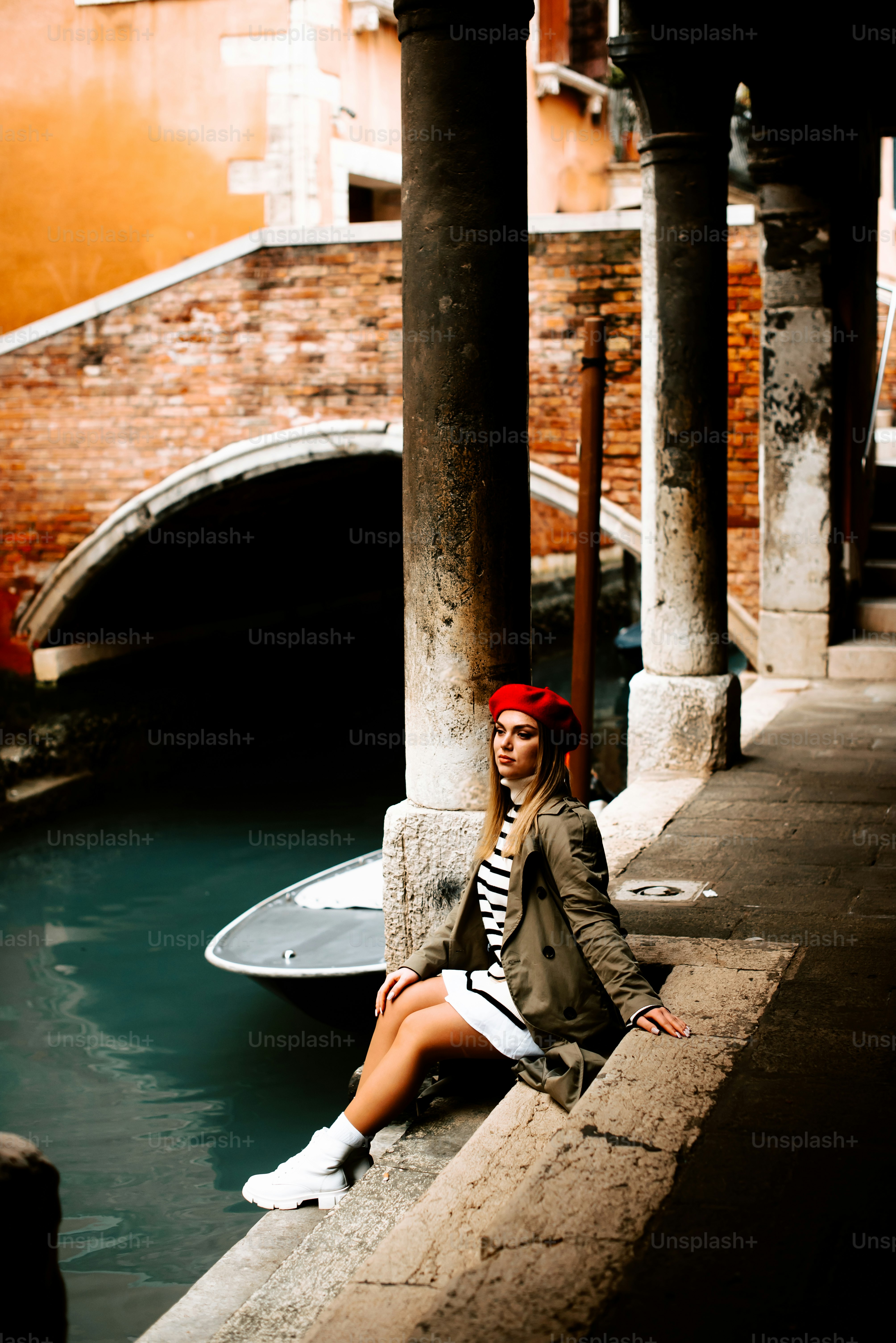 A woman sitting on a ledge next to a canal photo – Column Image on Unsplash