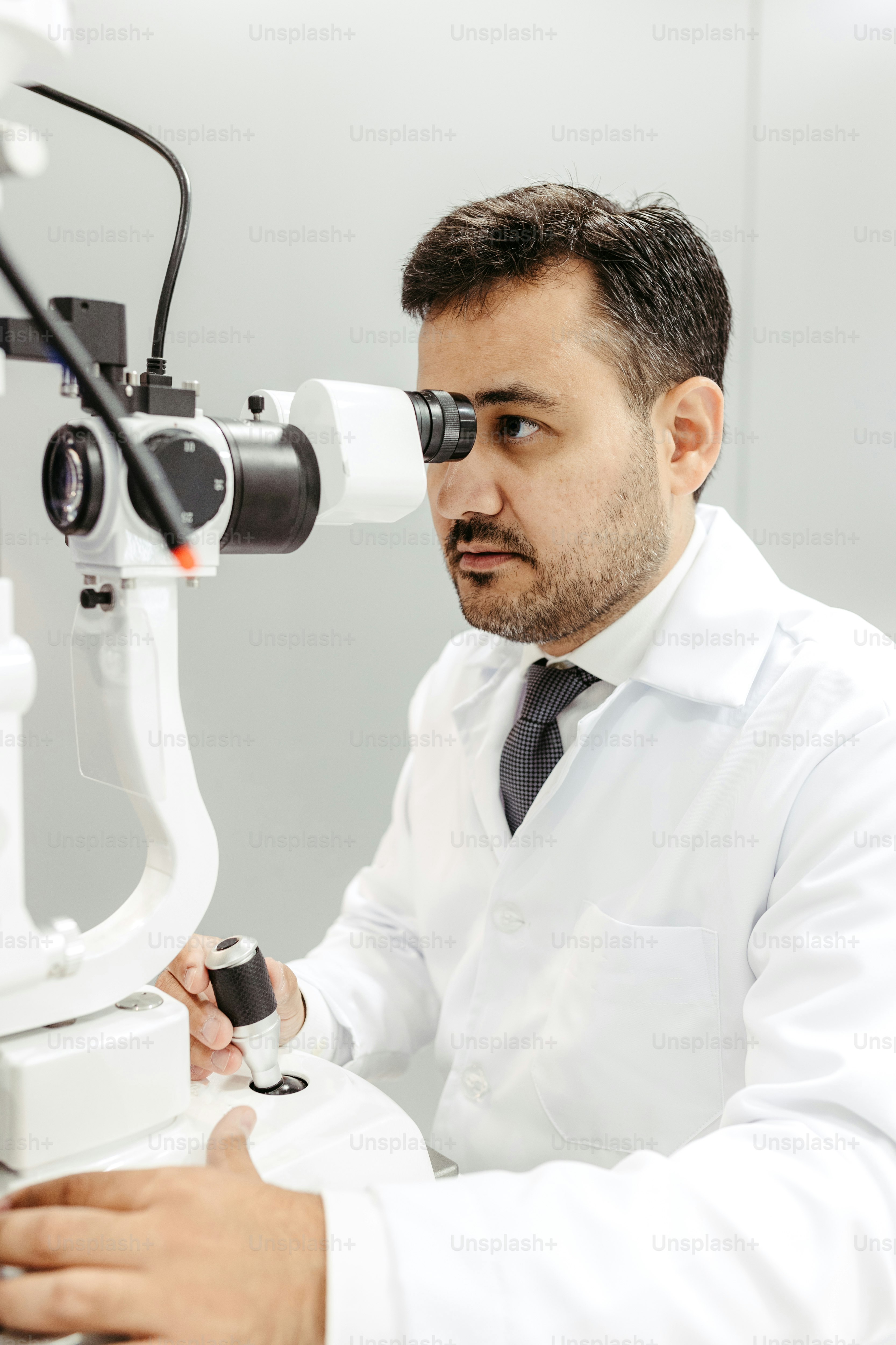 A man in a lab coat looking through a microscope photo – Optometrist ...