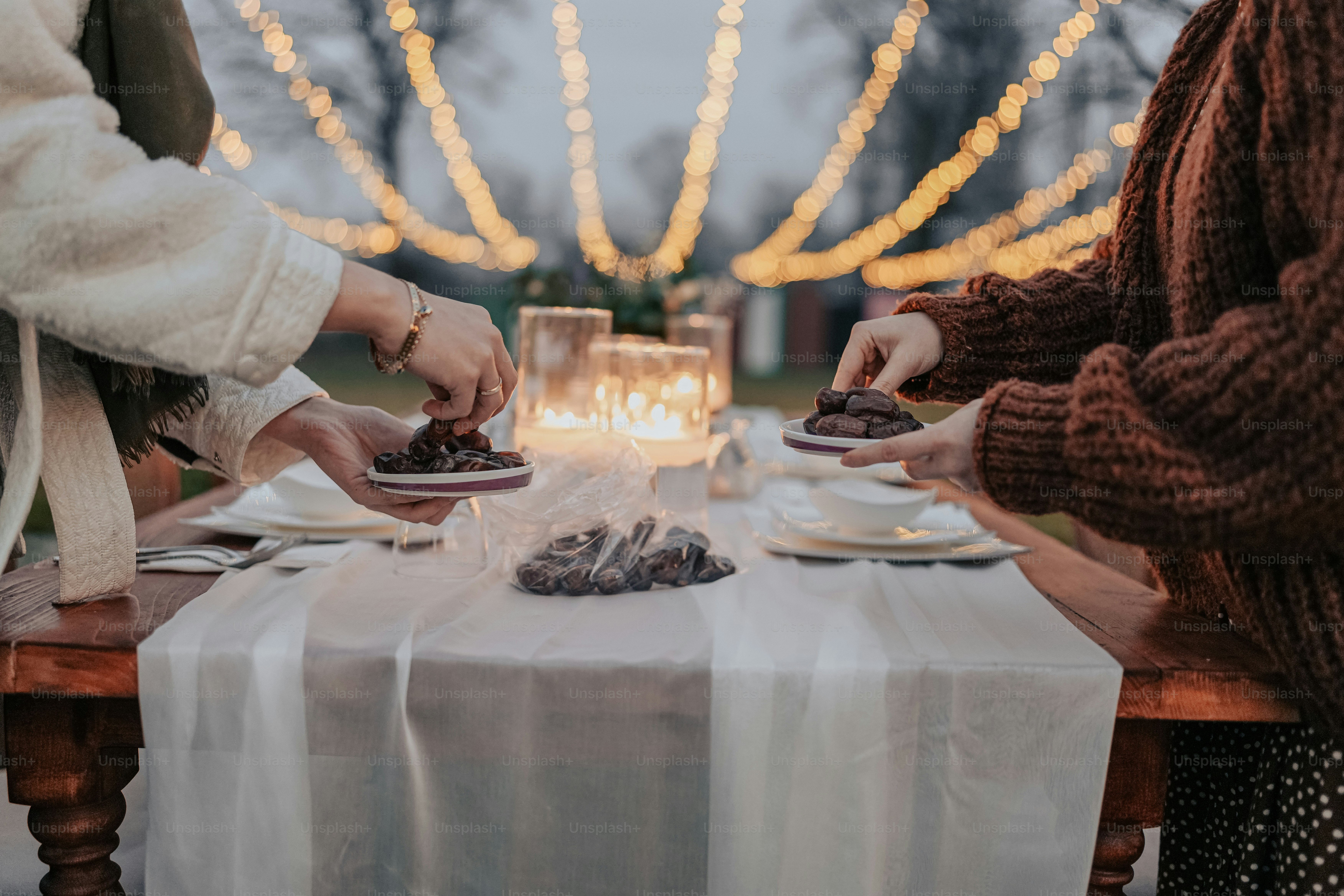 A couple of people standing over a table with plates of food photo ...