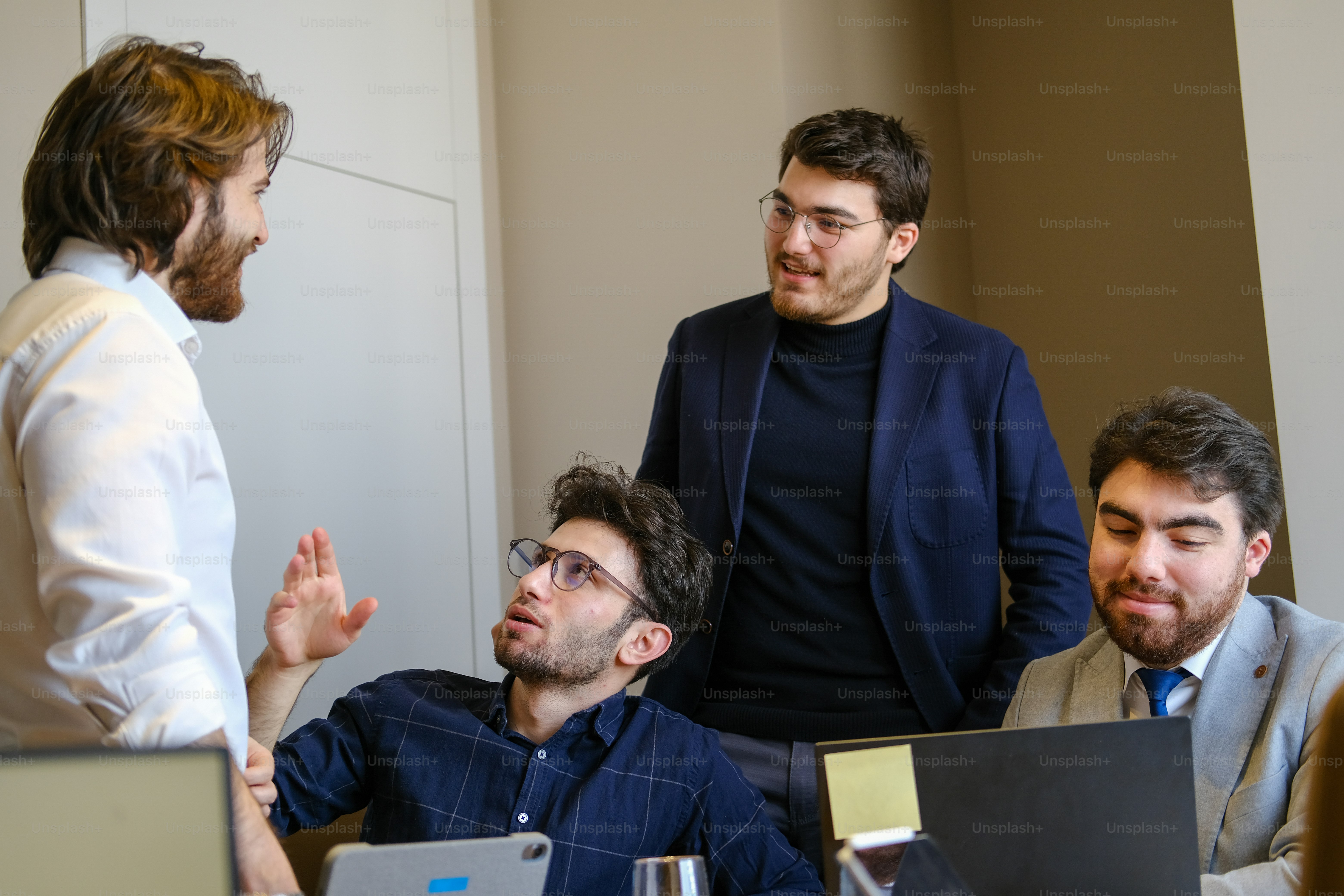 A group of men sitting around a table with laptops photo – Work group ...