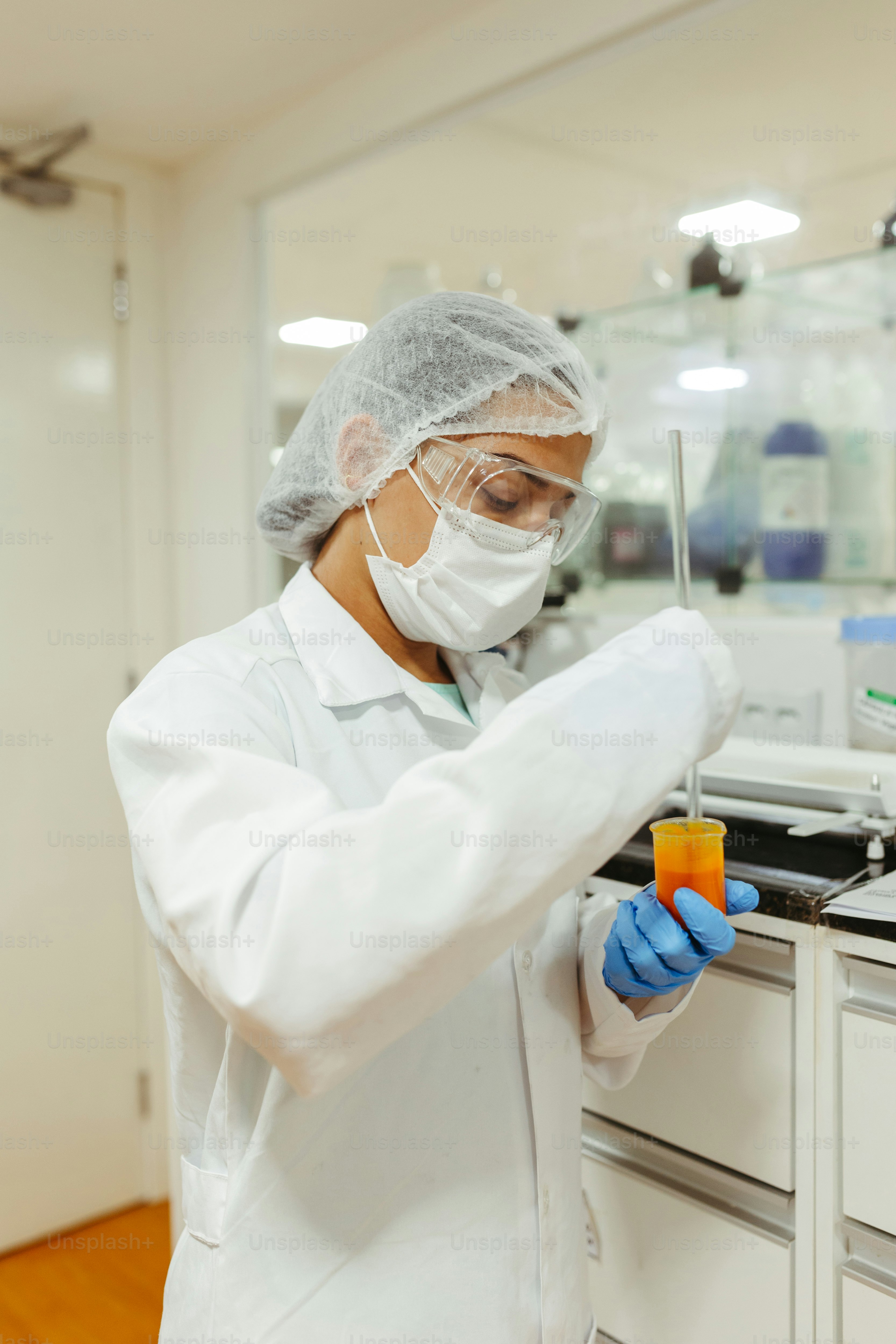 A person in a white coat and blue gloves holding a beaker photo ...