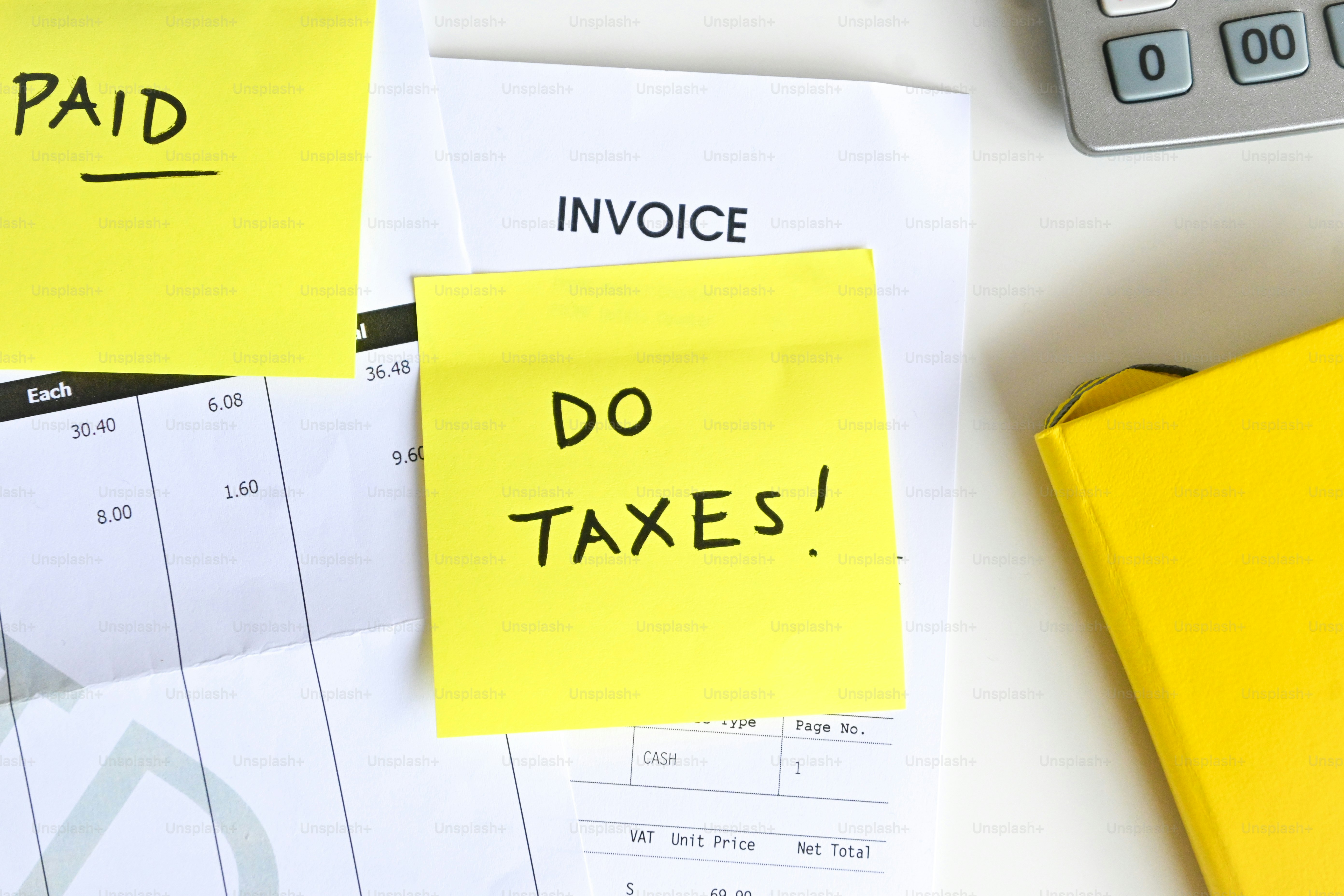 A yellow post it note with the words invoice and do taxes written on ...