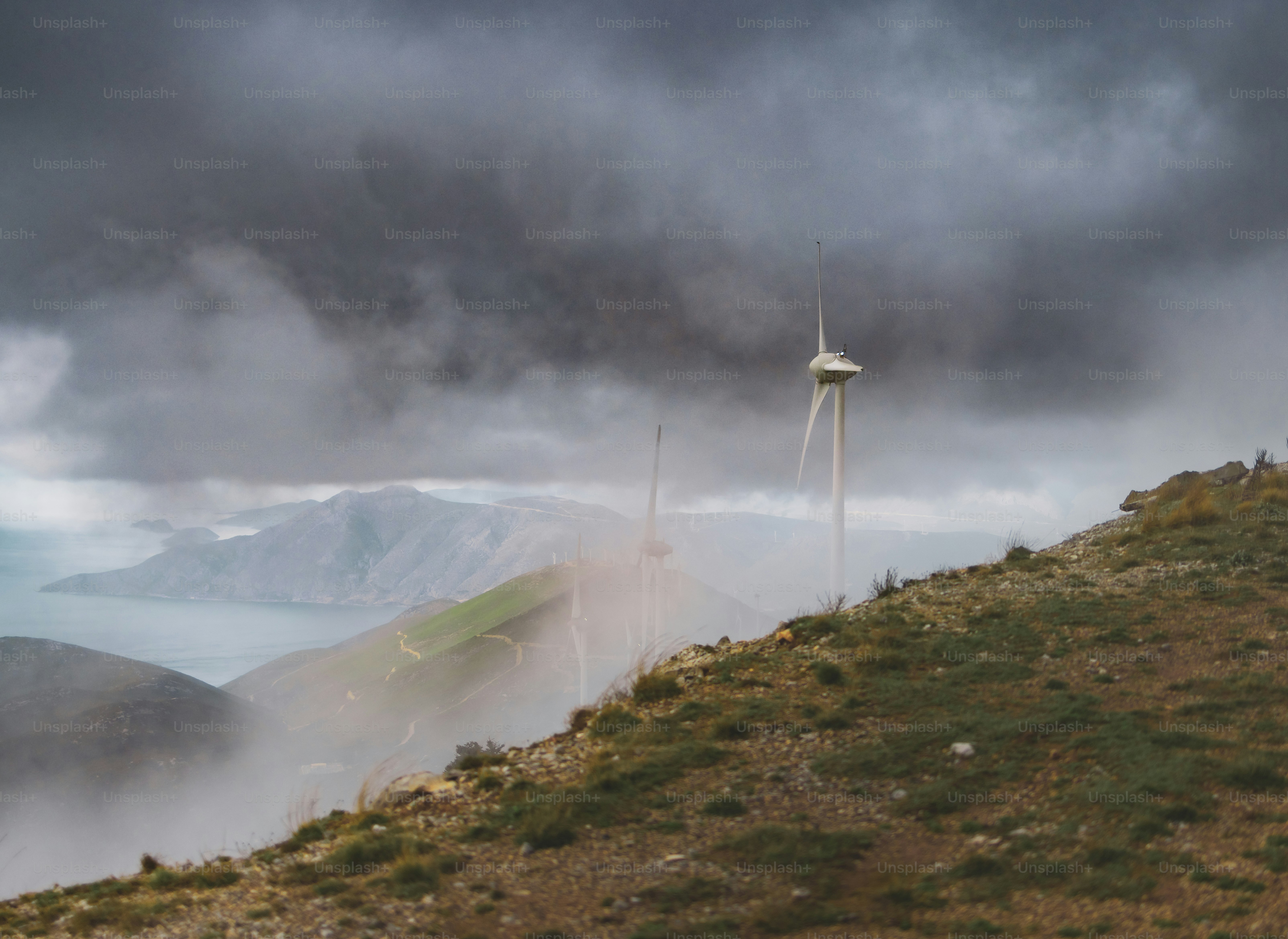 A wind turbine on a hill with a body of water in the background photo ...