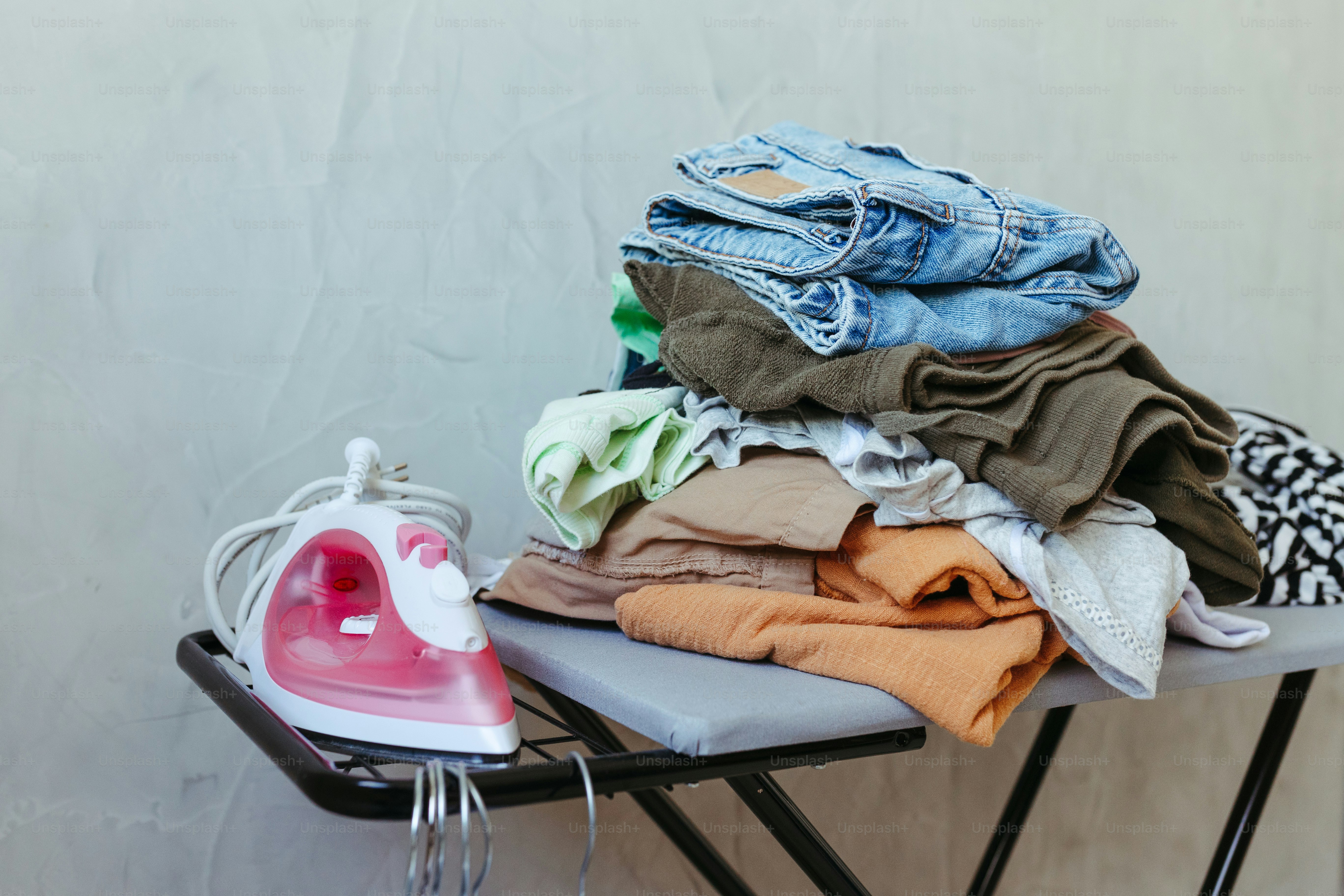 A ironing board with clothes on it next to a clothes rack photo ...