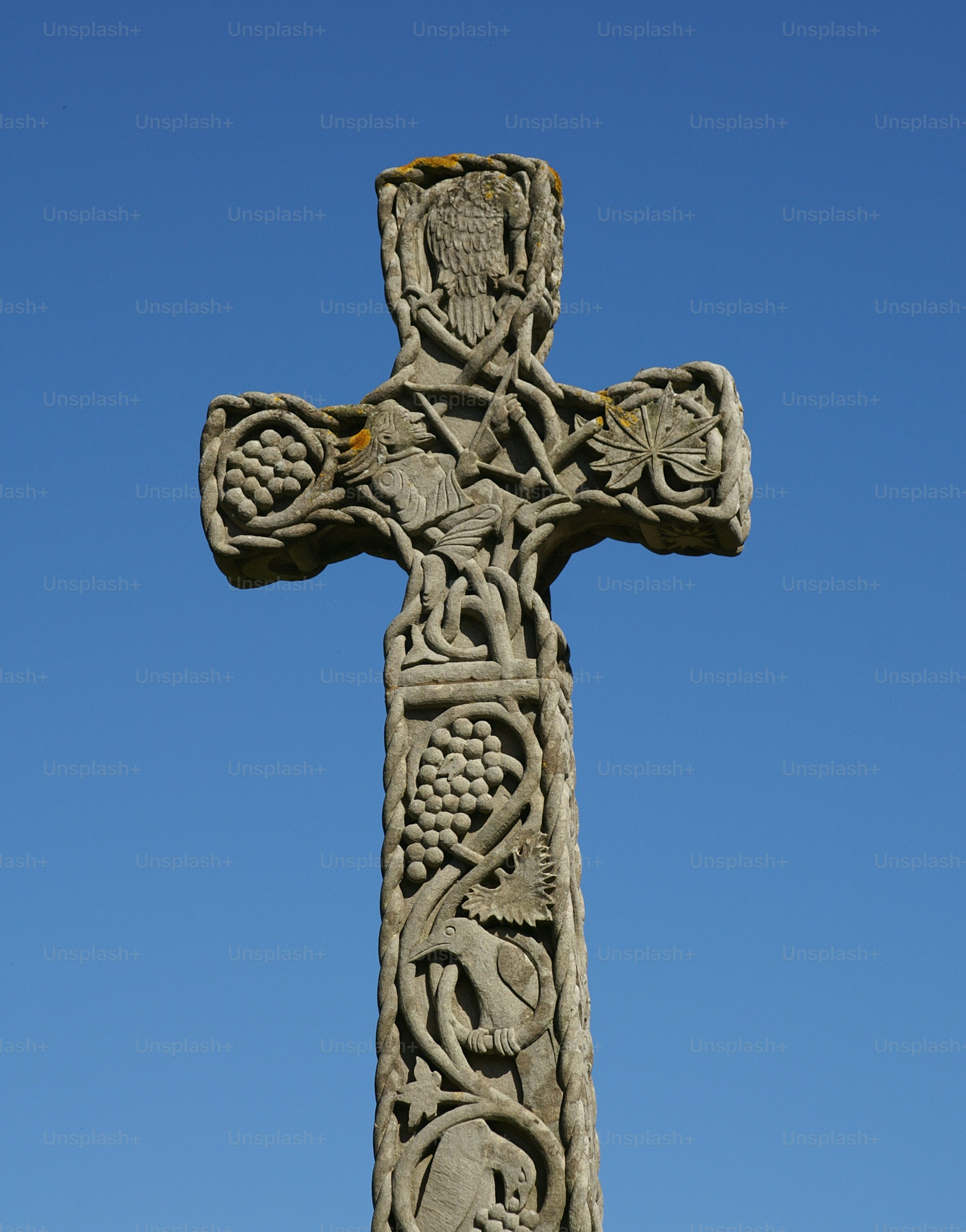 A stone cross with carvings on it against a blue sky photo – England ...