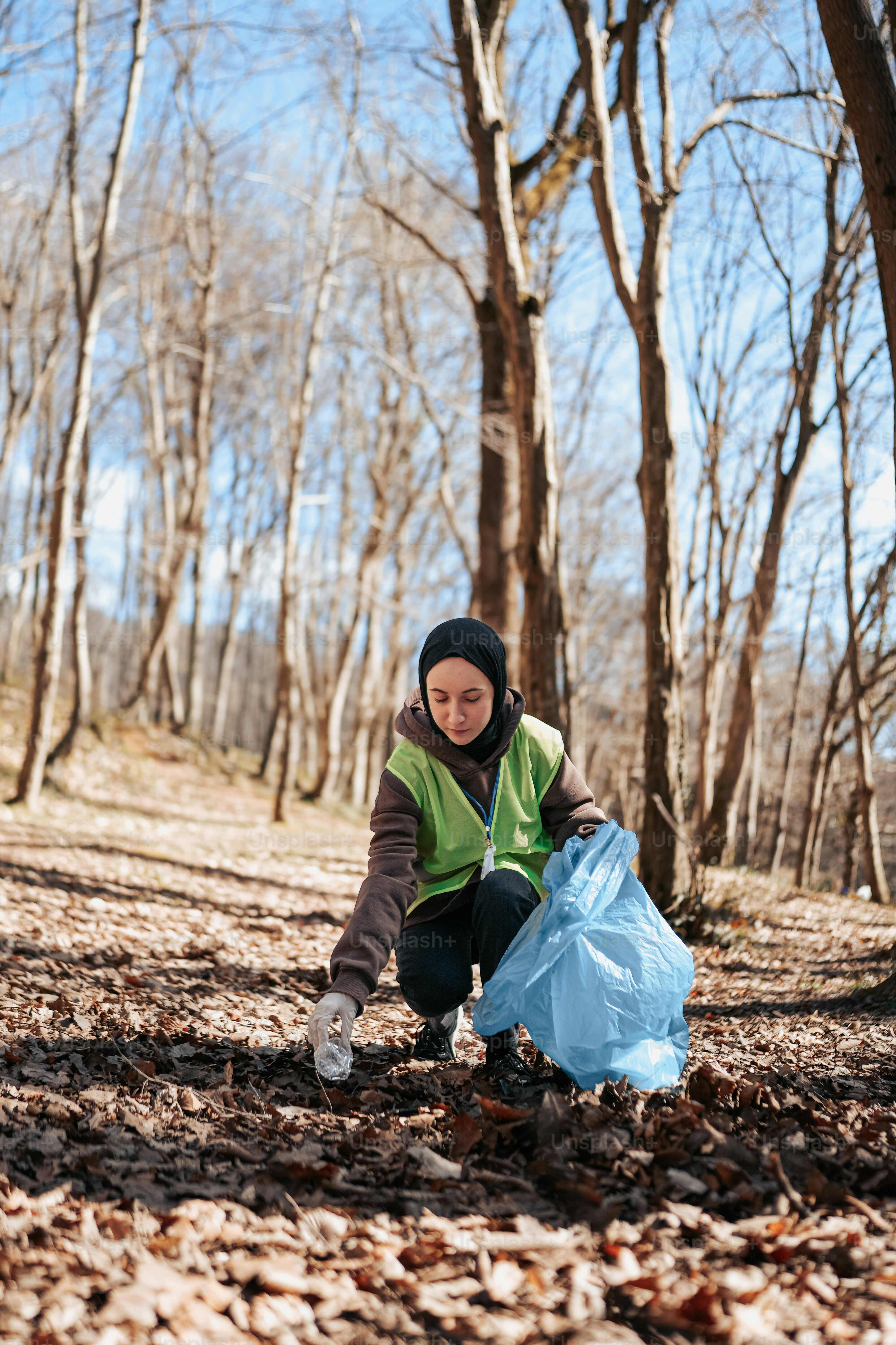 A woman crouches down to pick up trash in the woods photo ...
