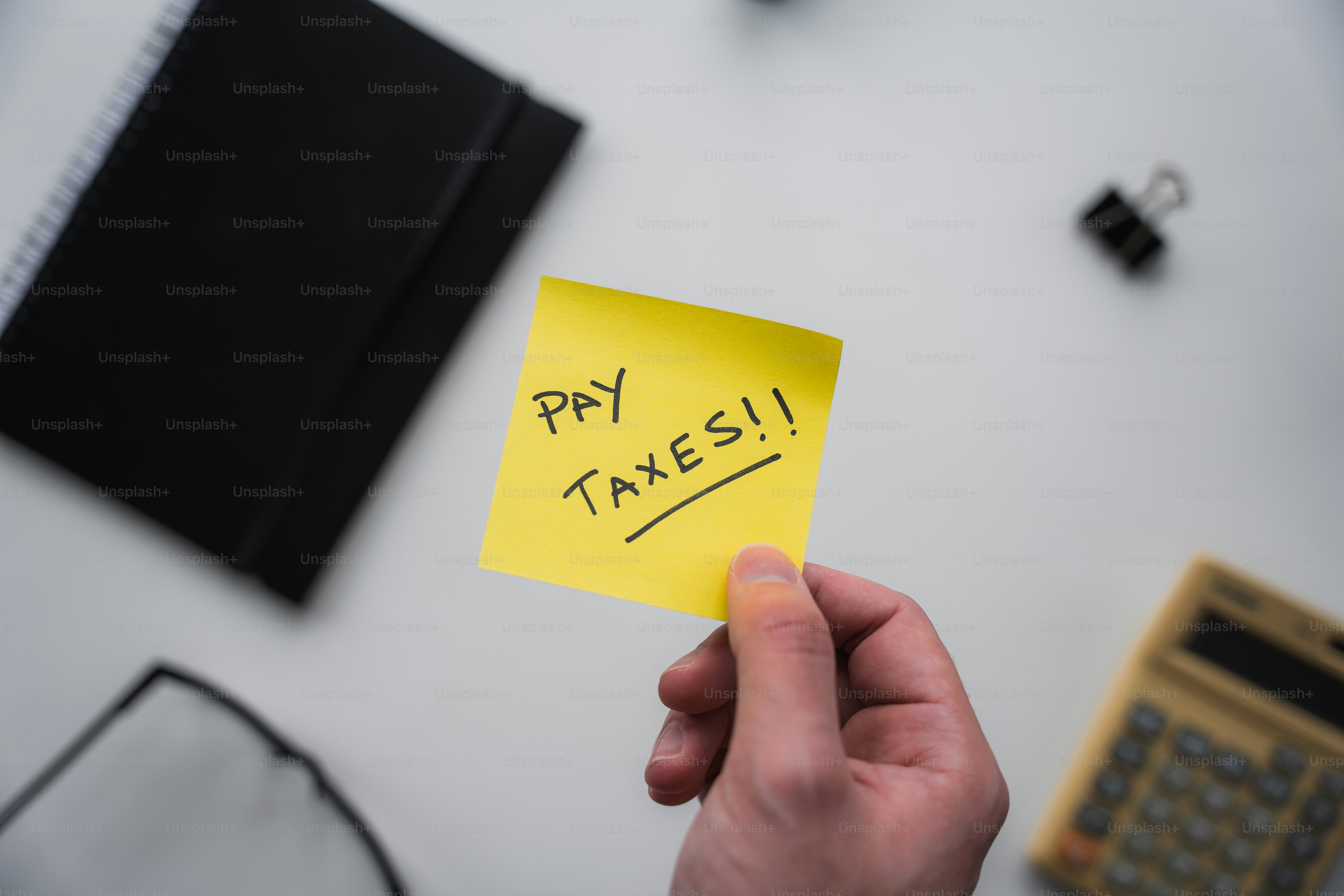 A person holding a sticky note with the words pay taxes written on it ...
