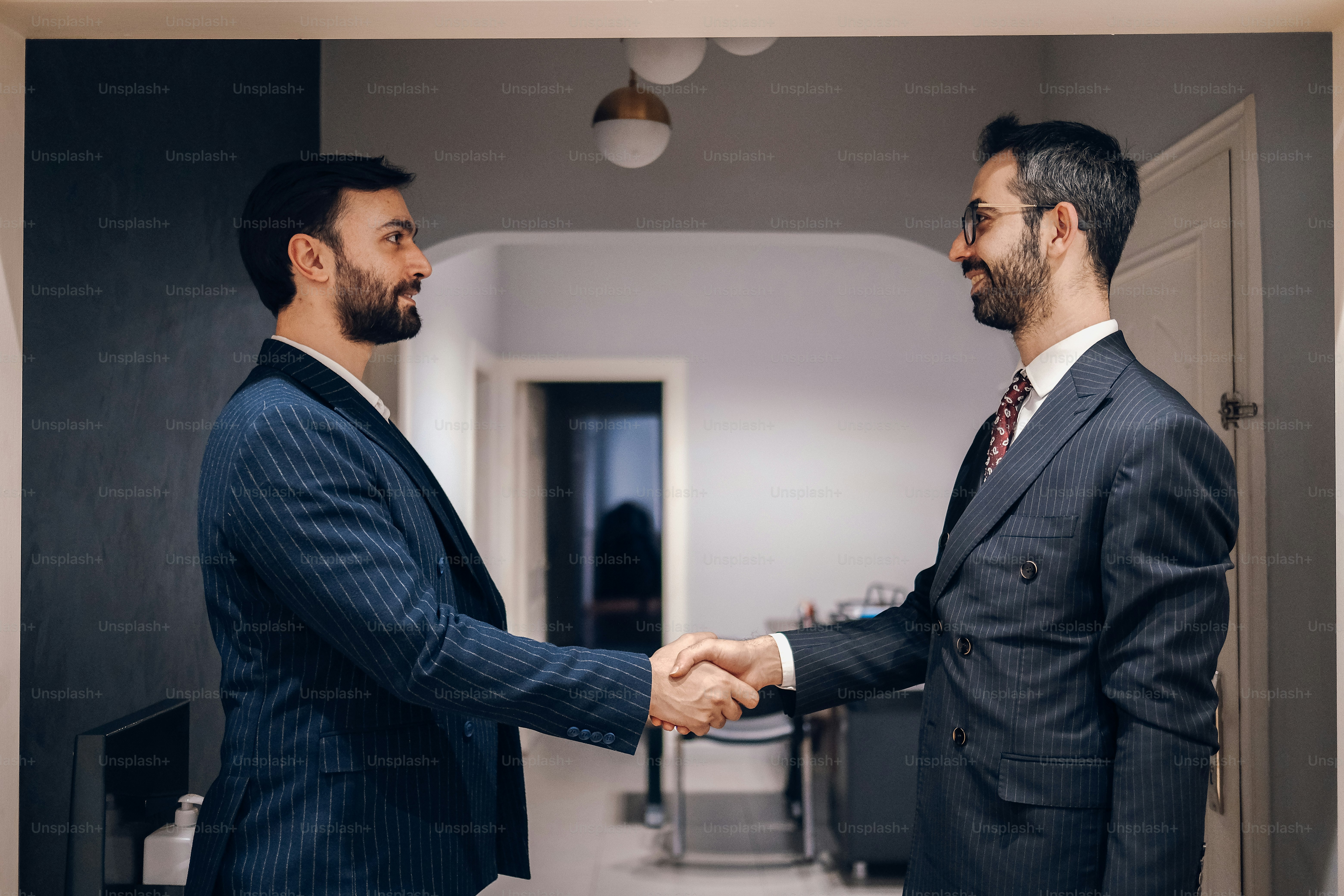 Two men in suits shaking hands in a hallway photo – Businessmen Image ...