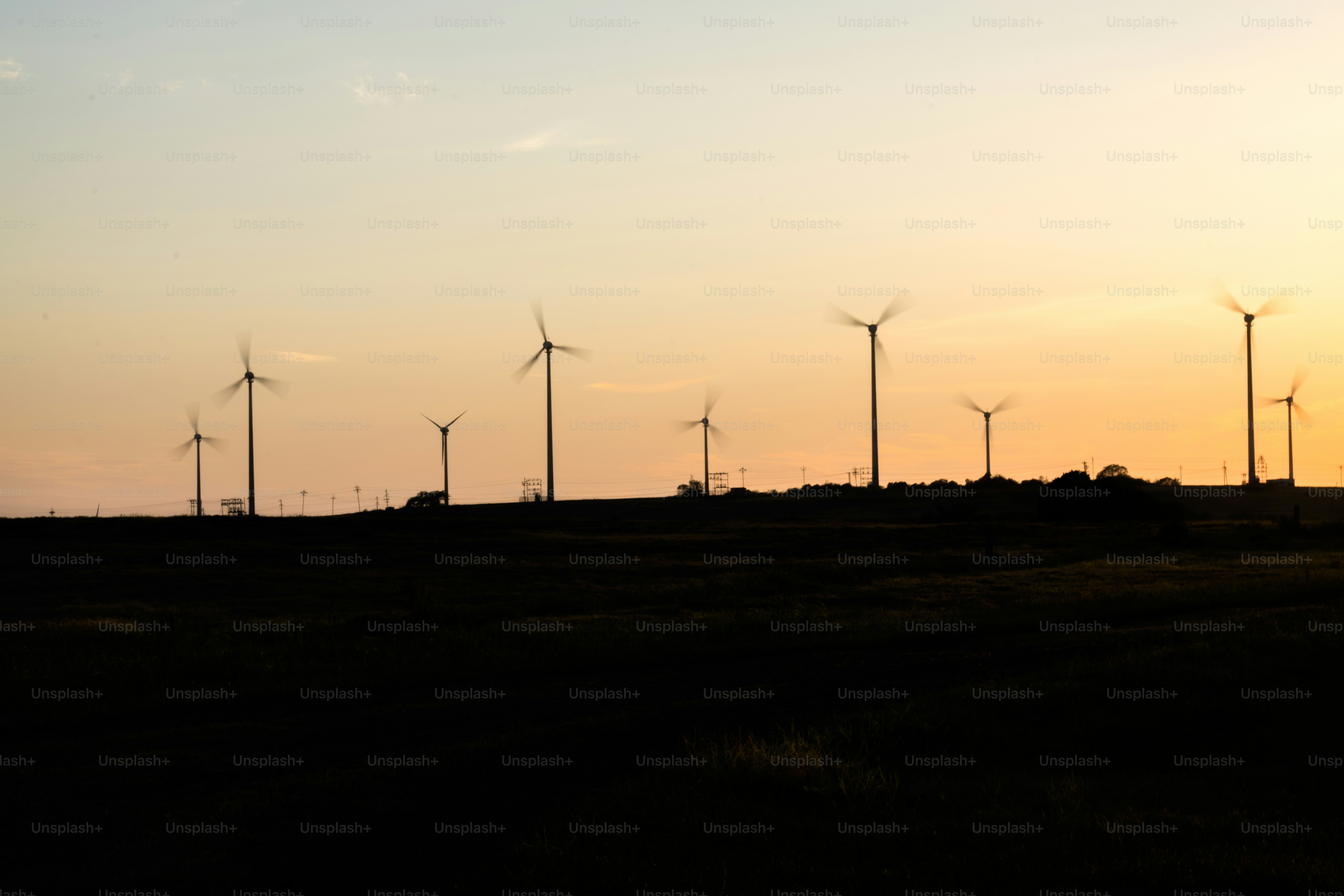 A row of windmills in a field at sunset photo – Wind power Image on ...