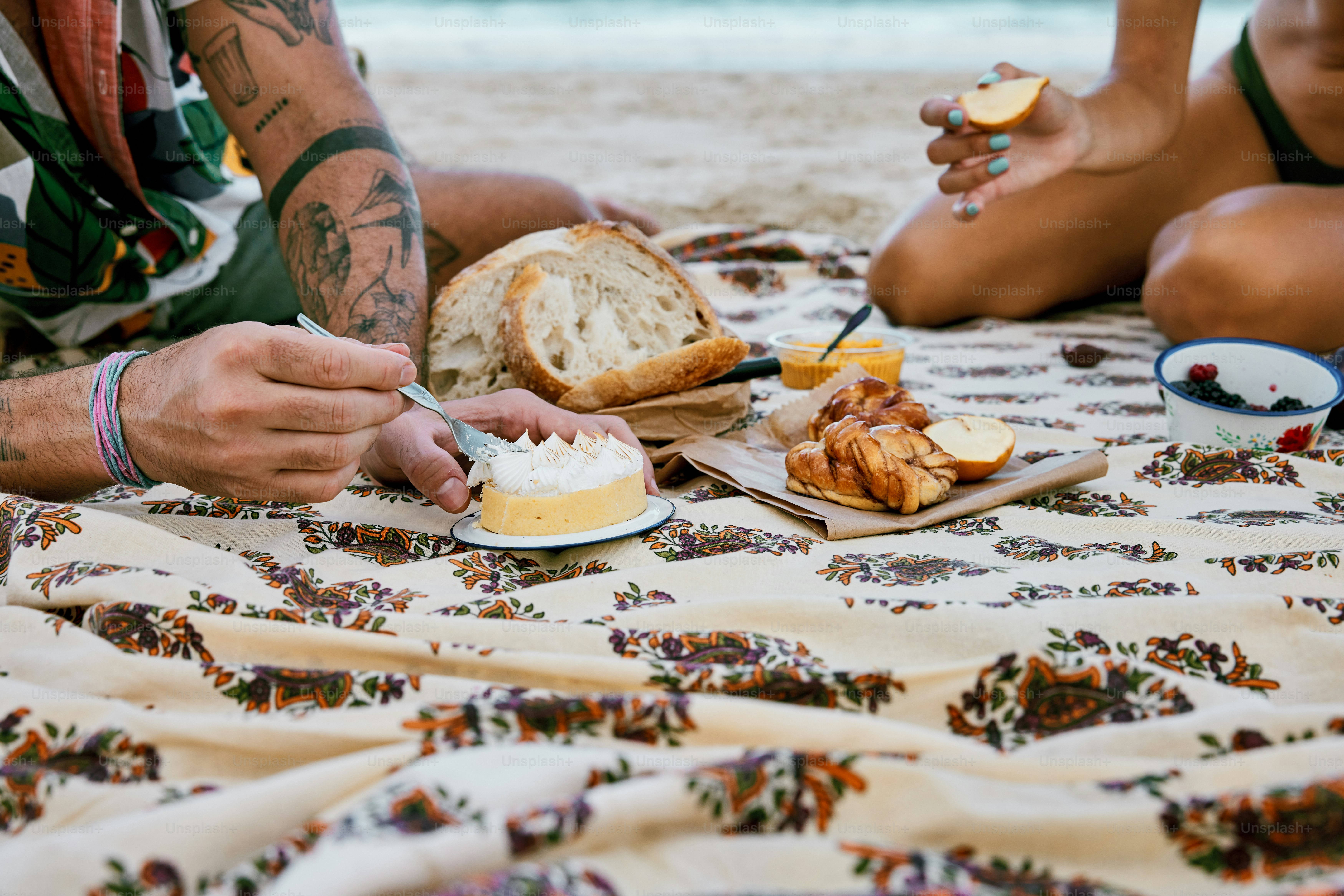 A couple of people sitting on a beach eating food photo – Food Image on ...