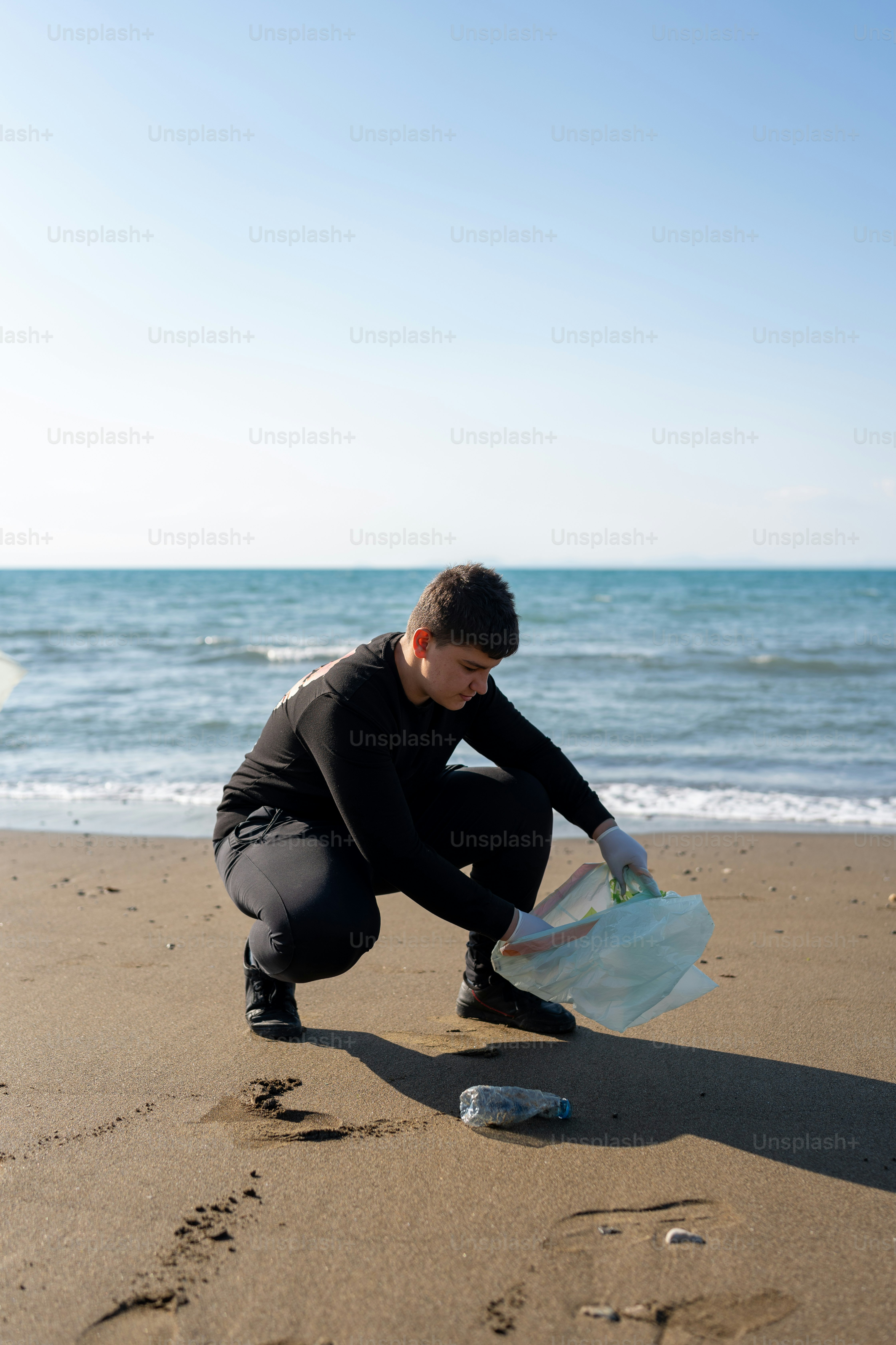 A man kneeling down on a beach next to the ocean photo – Litter picking ...