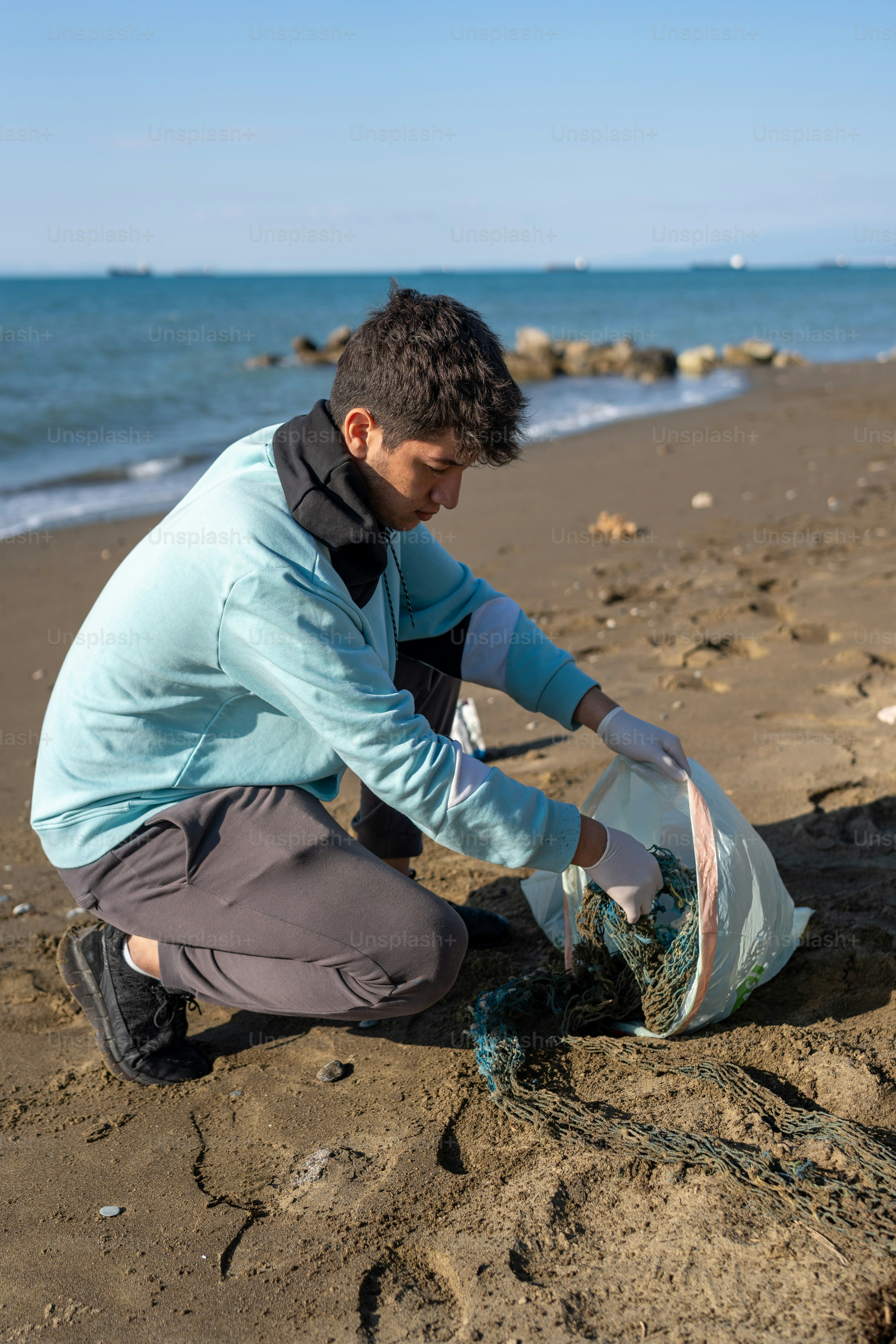 A man kneeling down on a beach next to the ocean photo – Clearing Image ...