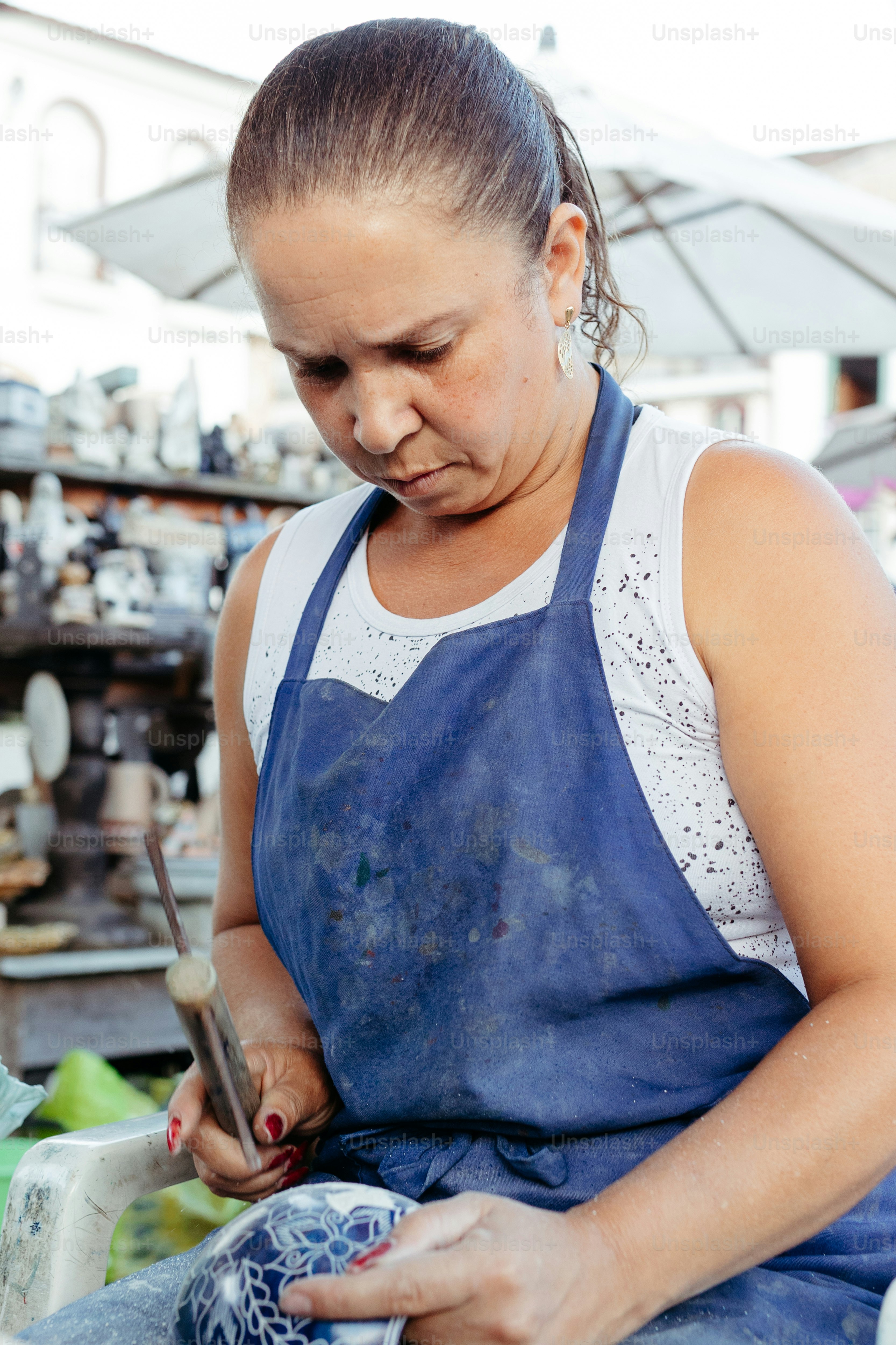 A woman in a blue apron working on a piece of pottery photo – Clay ...