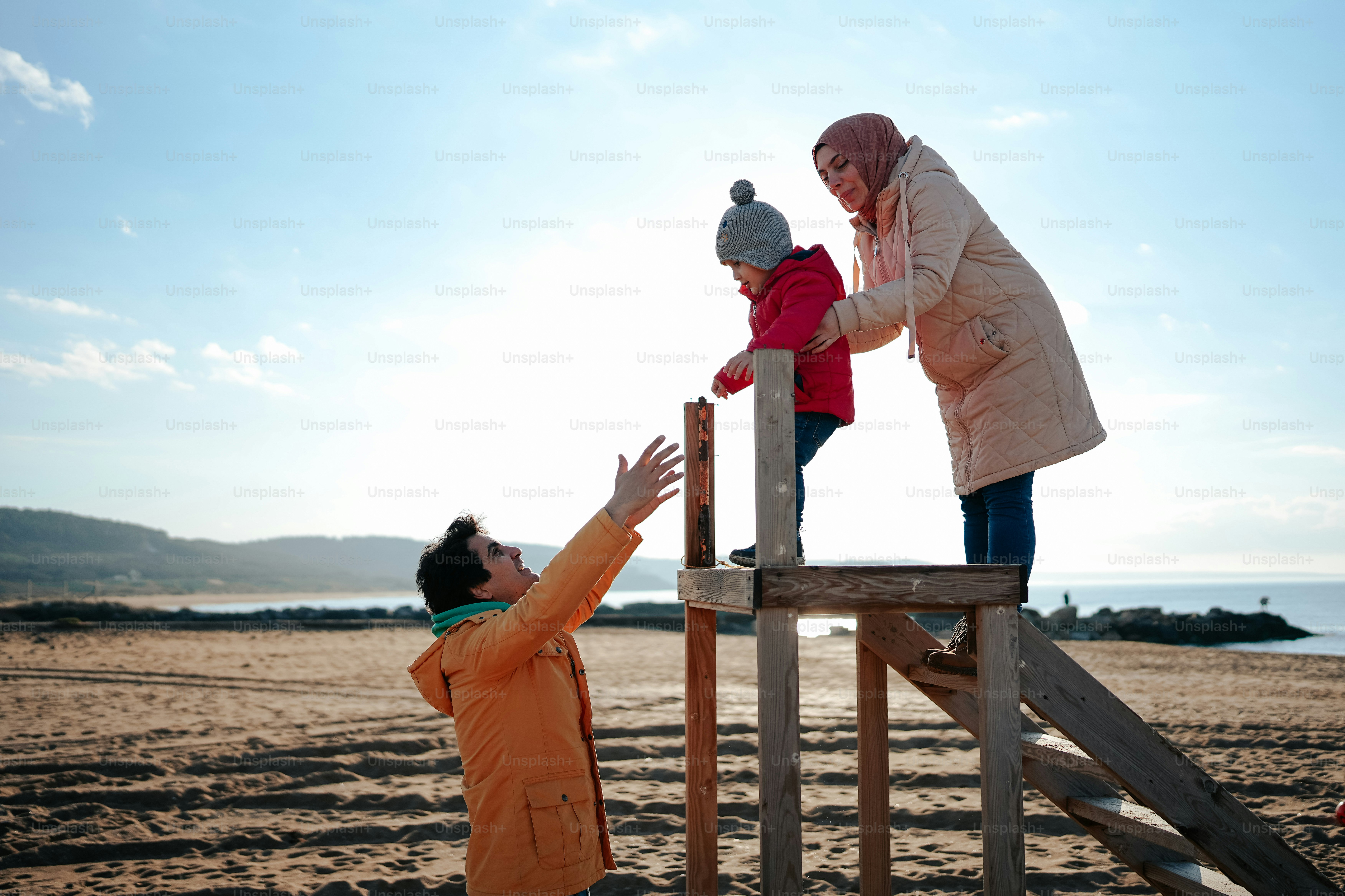 A woman helping a child climb a wooden structure photo – Beach Image on ...