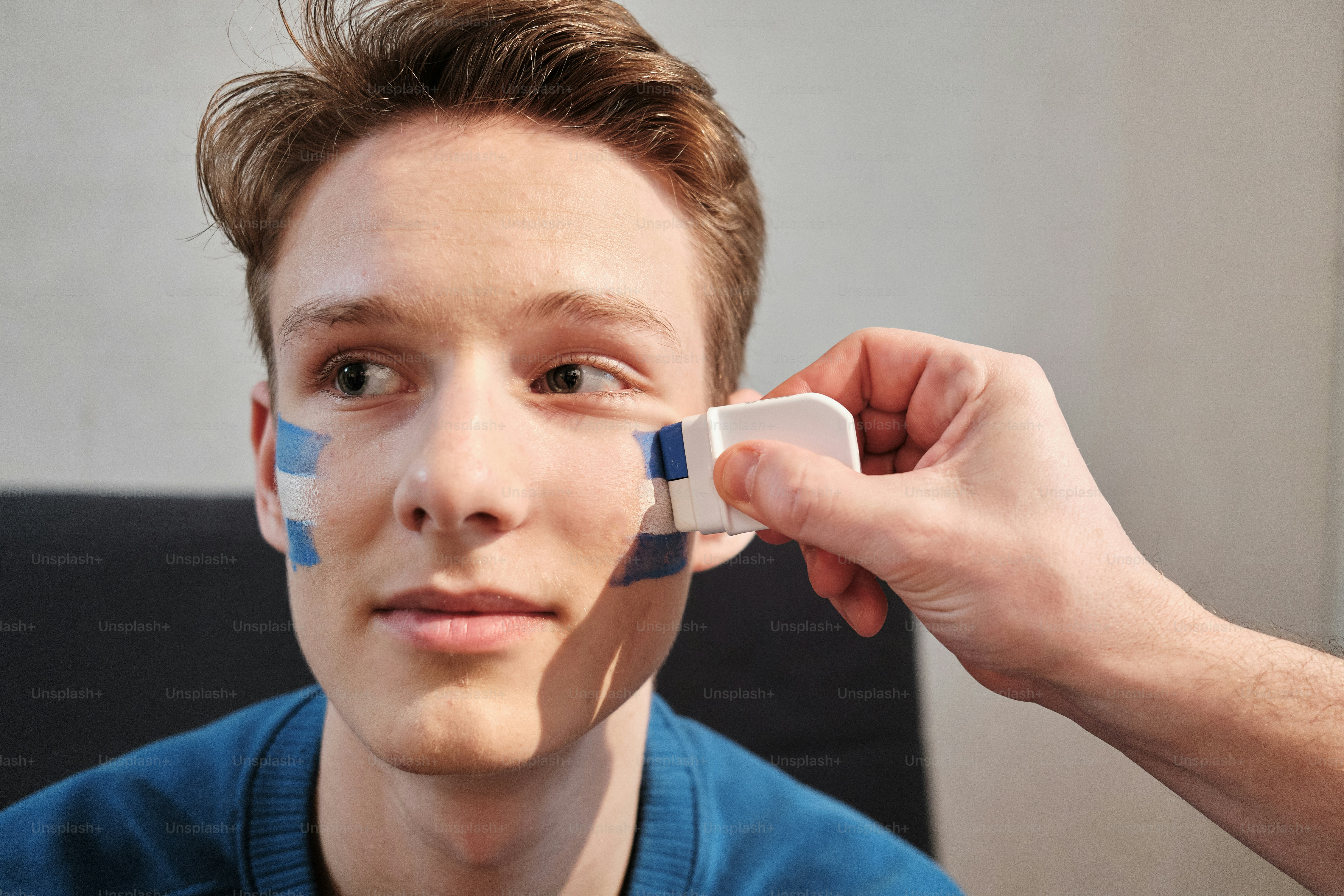 A young man is putting a blue and white face paint on his face photo ...