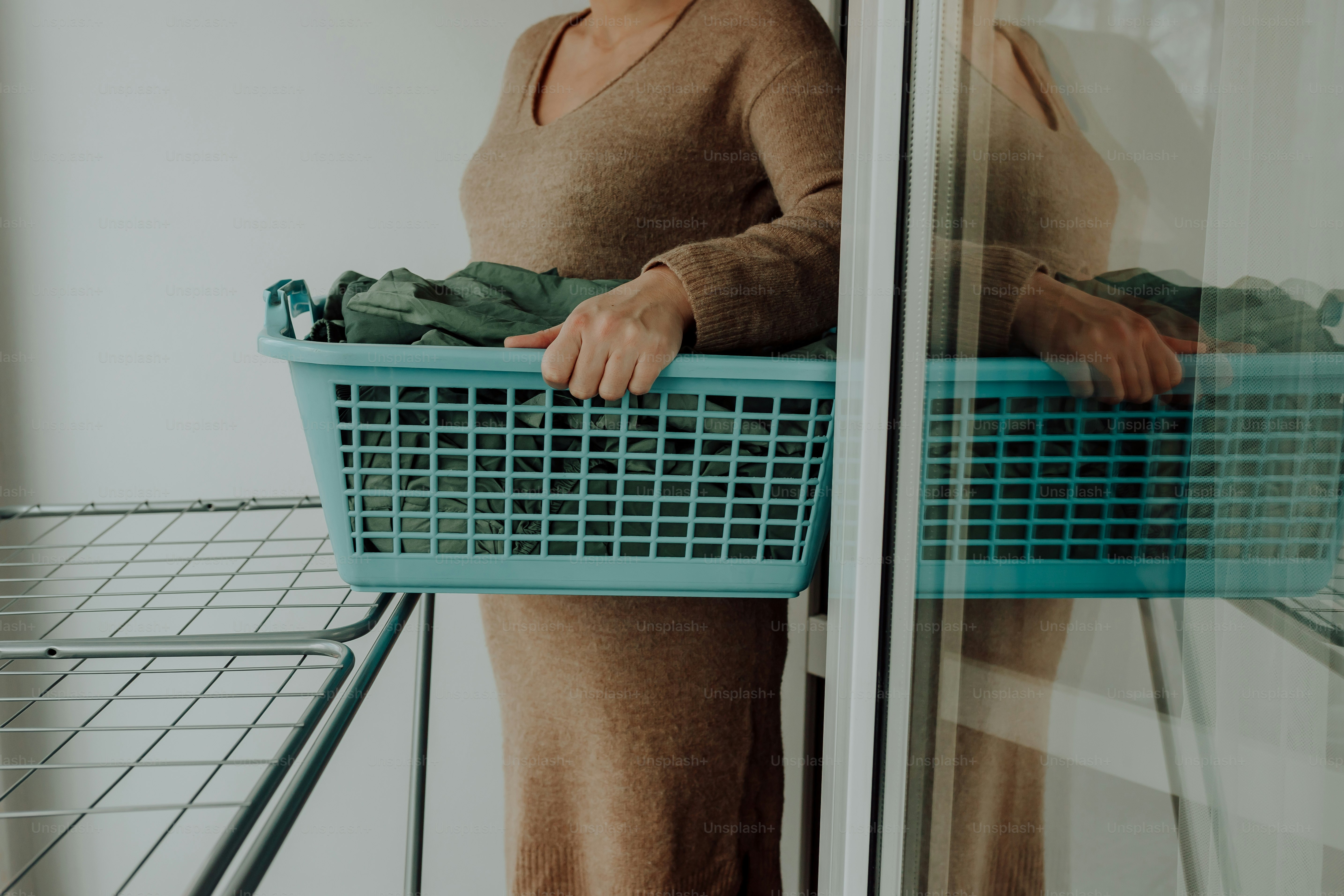 A woman holding a laundry basket in front of a window photo – Cleaning ...