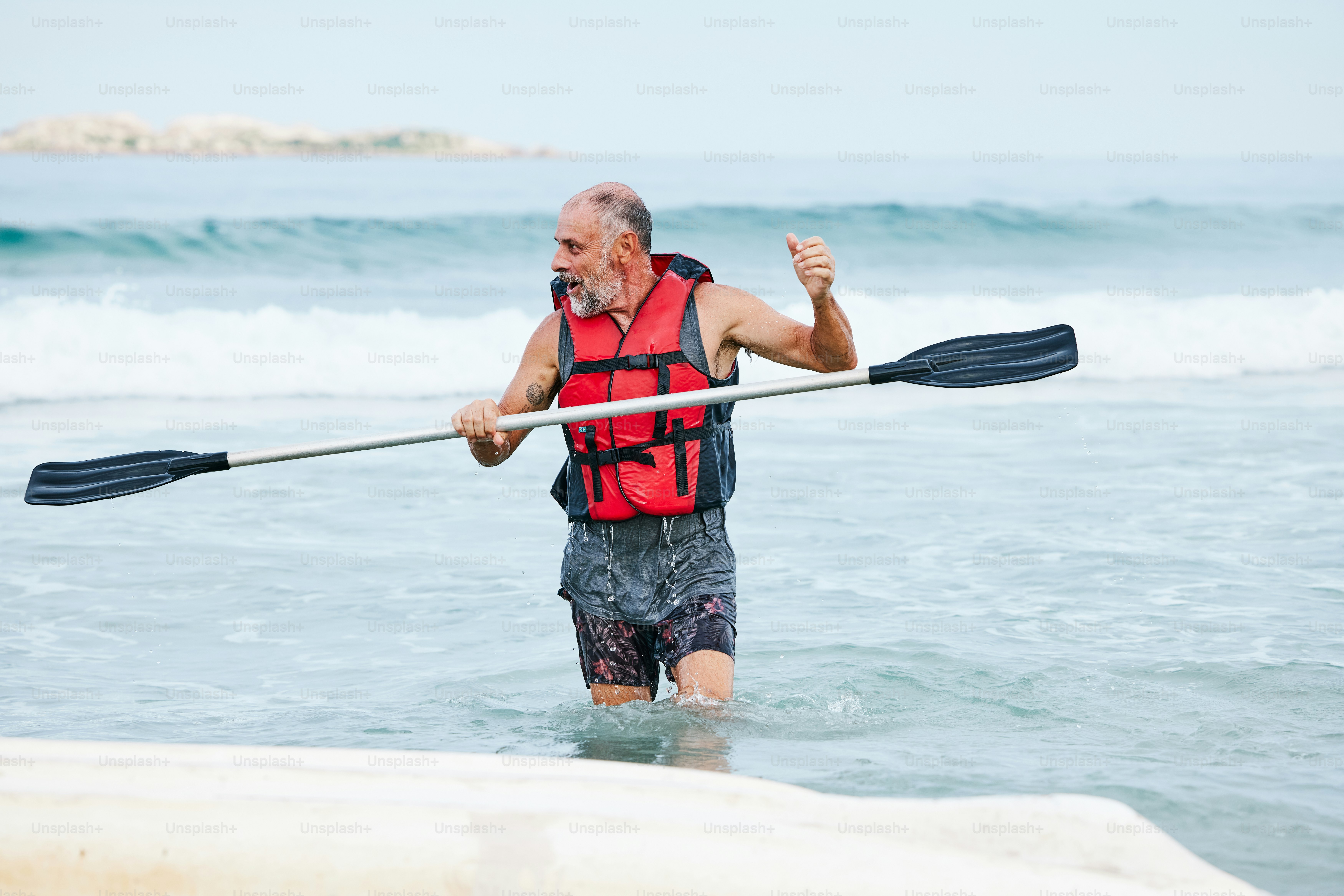 A man in a life jacket paddling a canoe in the ocean photo – Senior ...