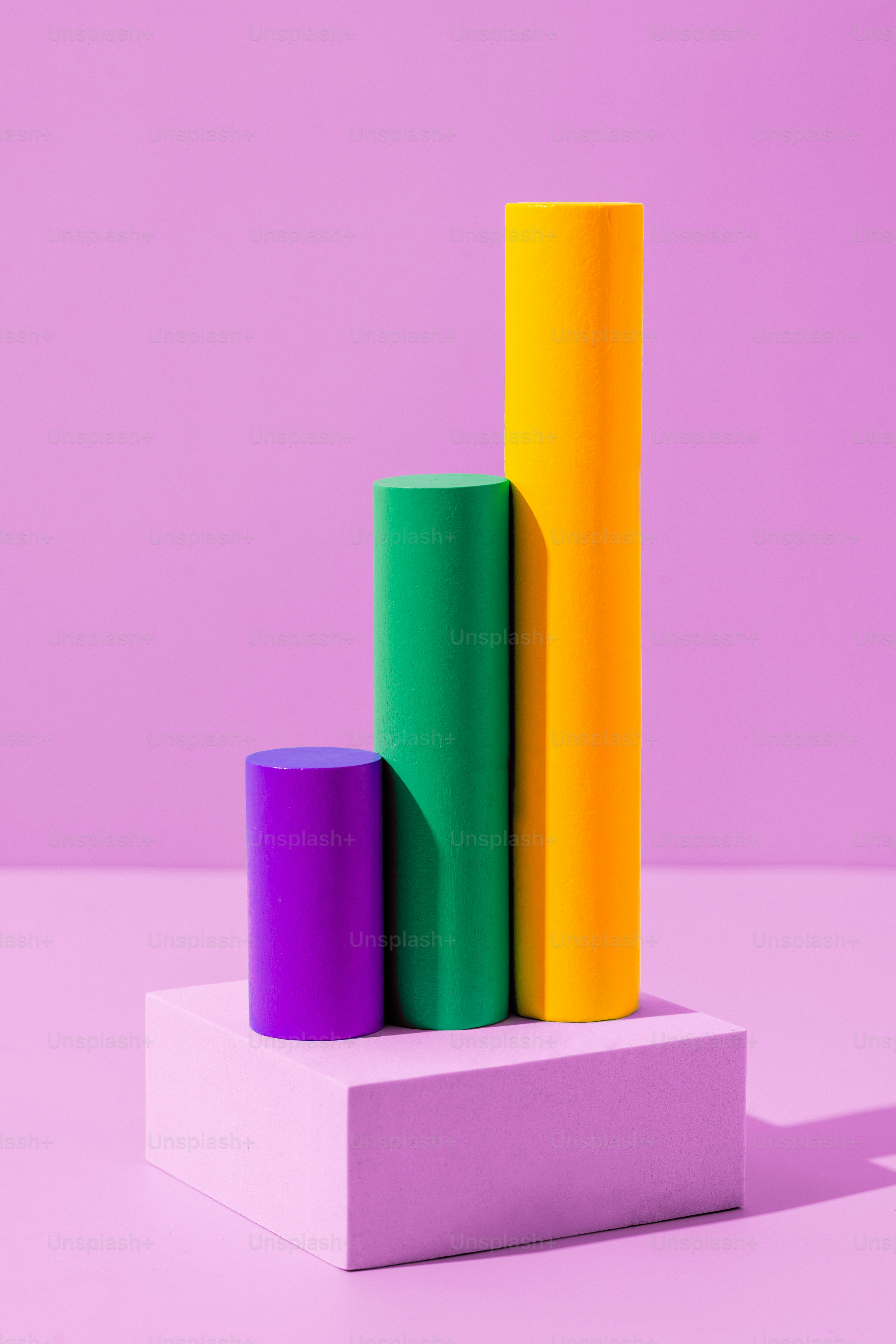 A stack of three different colored cylinders on a pink surface photo ...