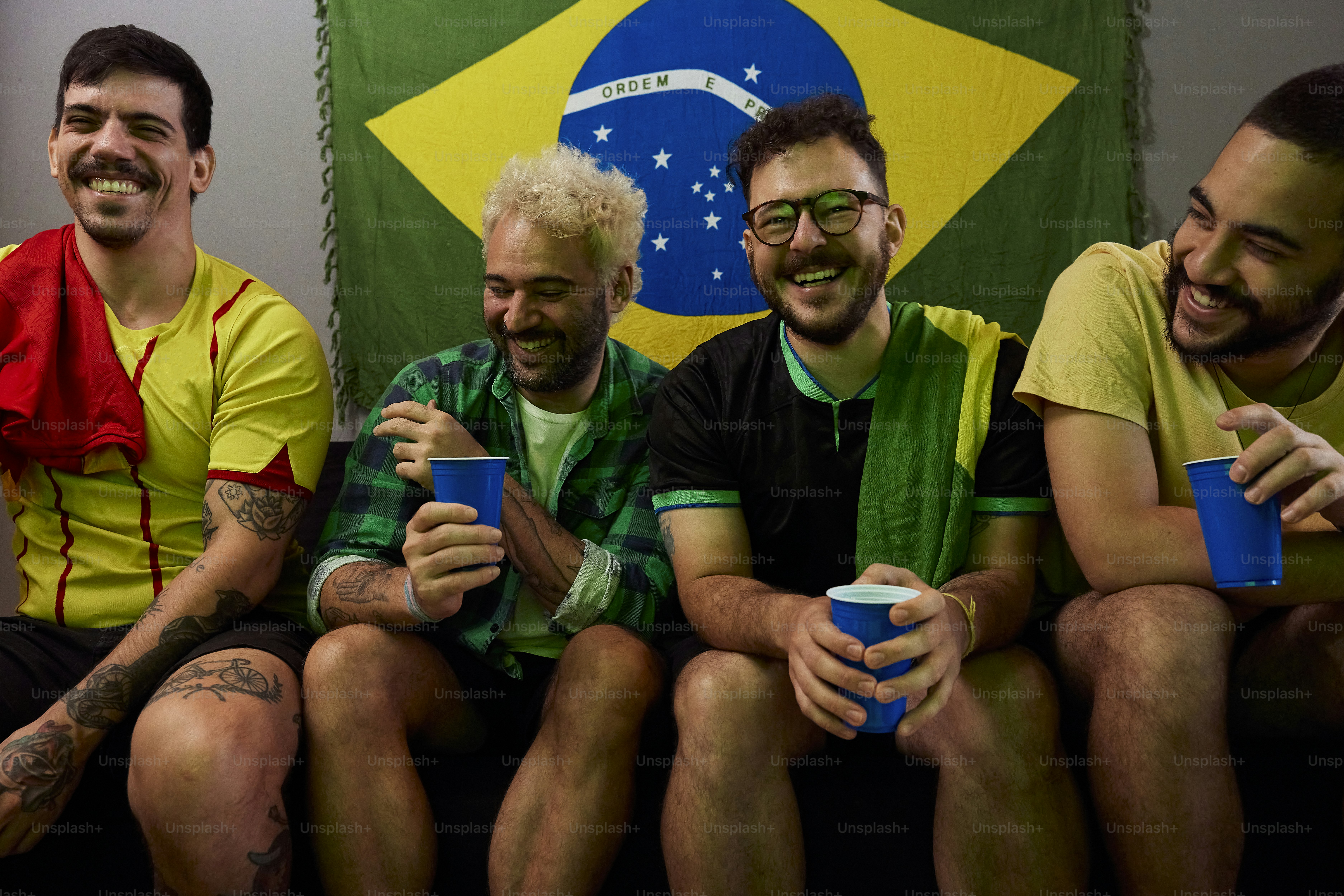A group of men sitting next to each other photo – Men watching tv Image ...