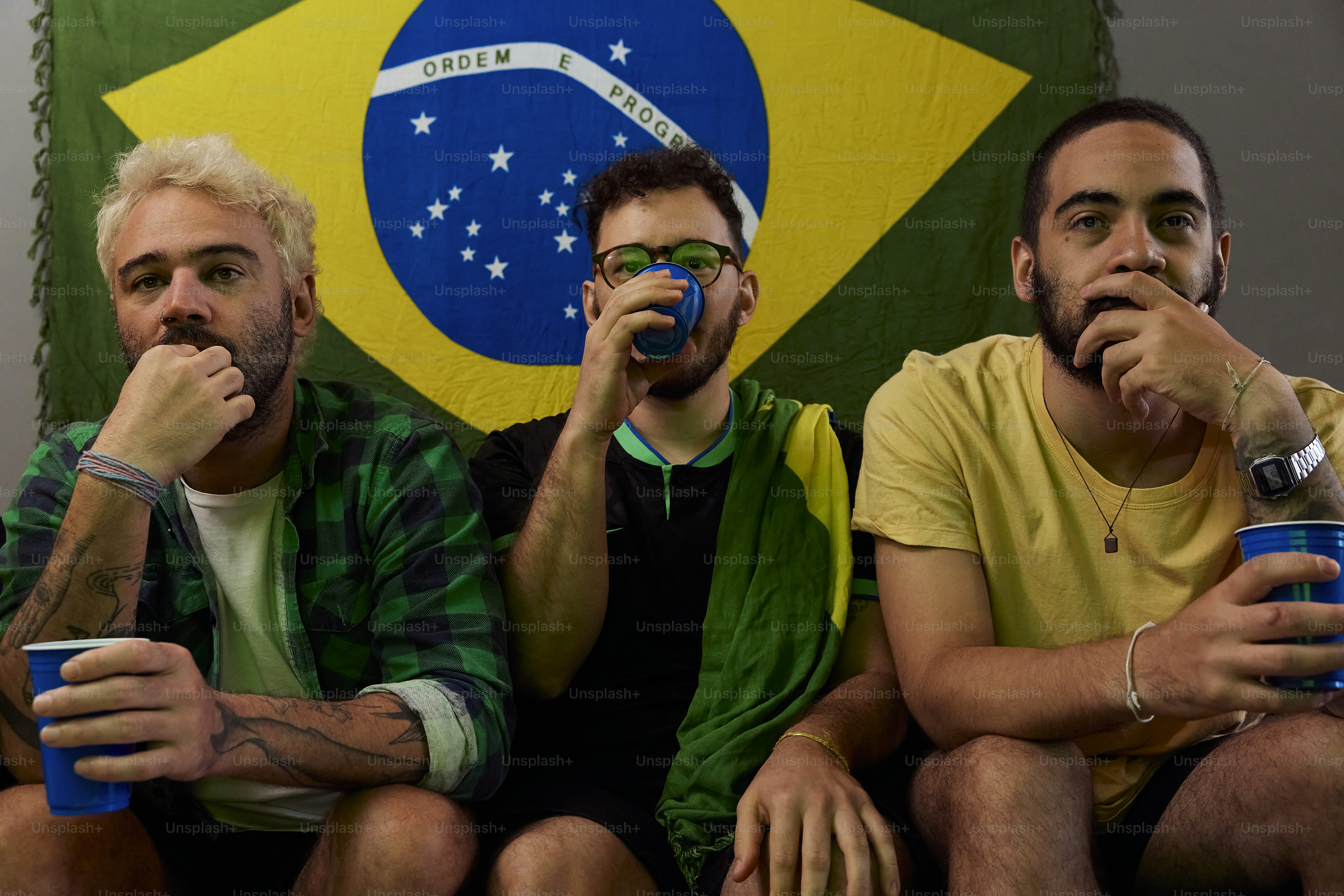 A group of men sitting next to each other photo – Men watching tv Image ...