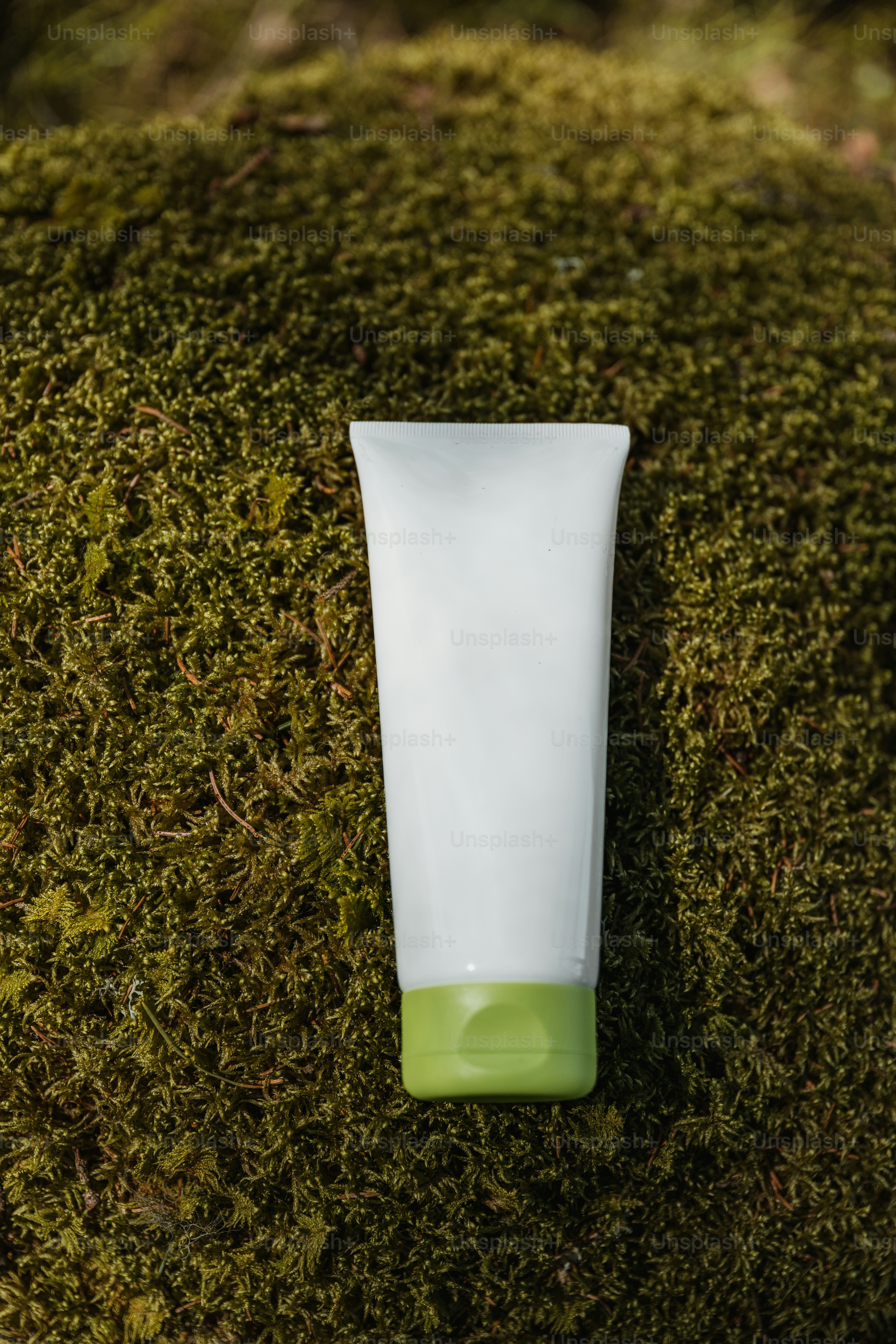 A tube of cream sitting on top of a moss covered ground photo – Mockup ...