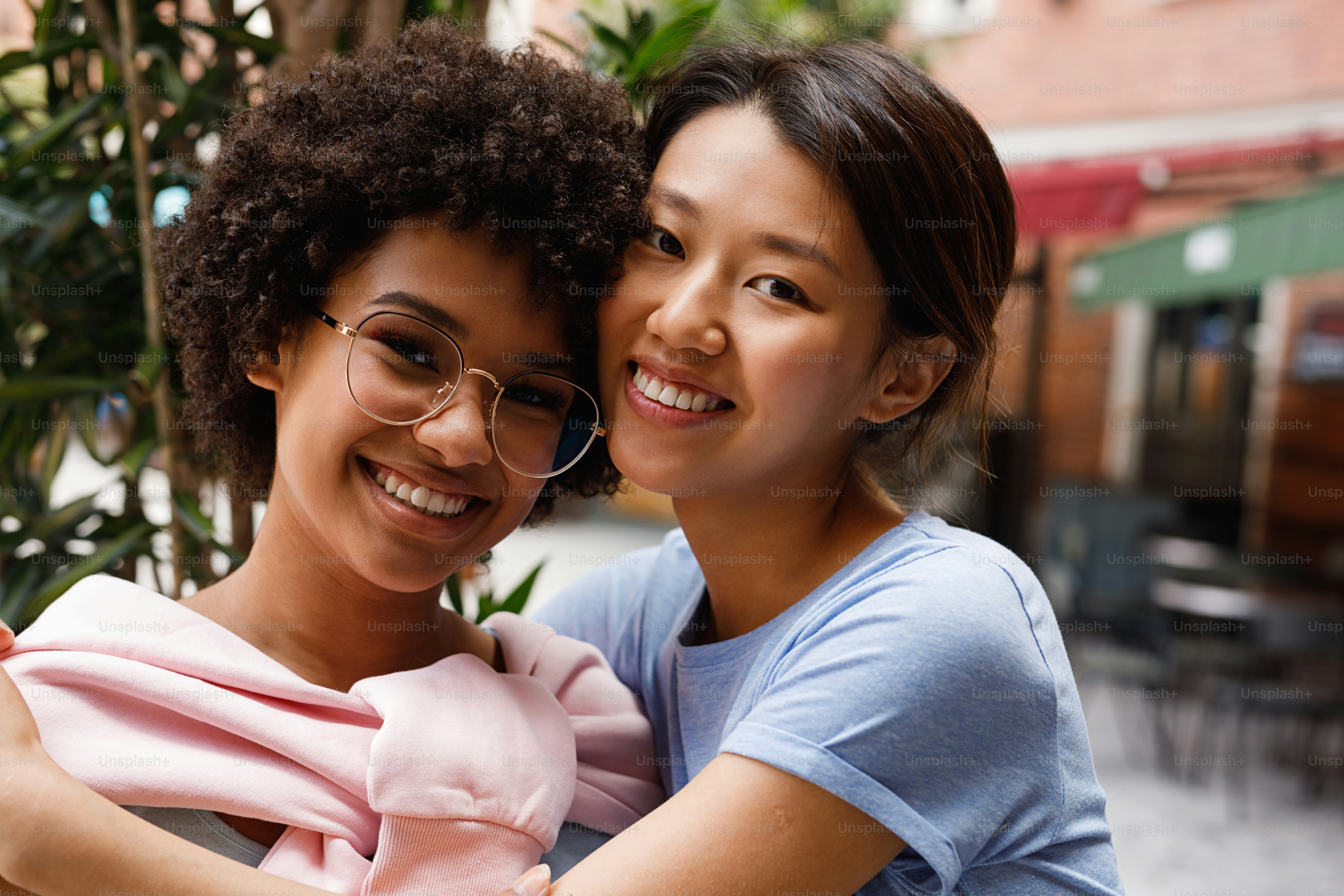 Two smiling friends looking at a camera, standing outdoors photo ...