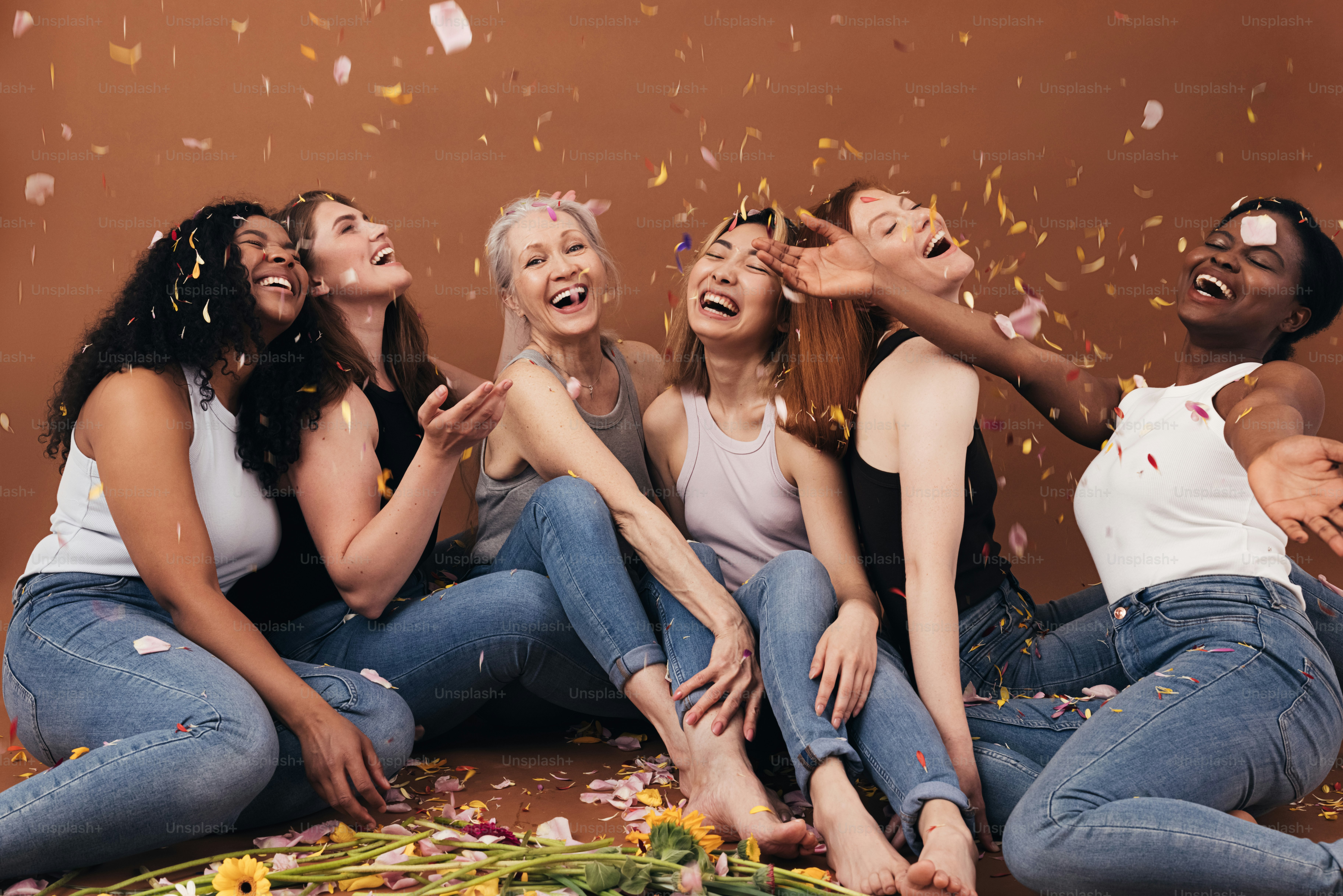 Group of six laughing women of different ages sitting under falling ...