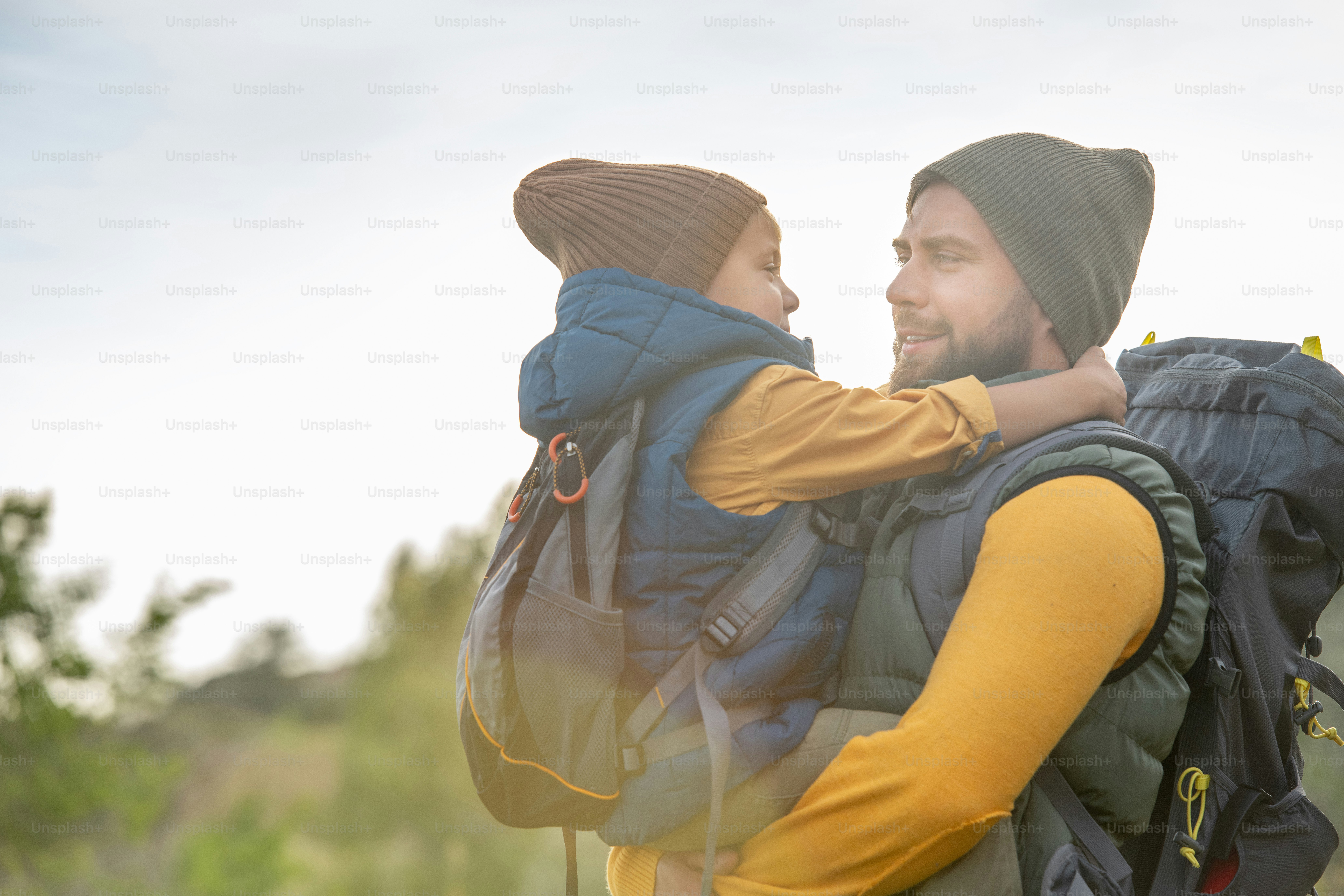 Young affectionate father with backpack holdng his cute little son on ...