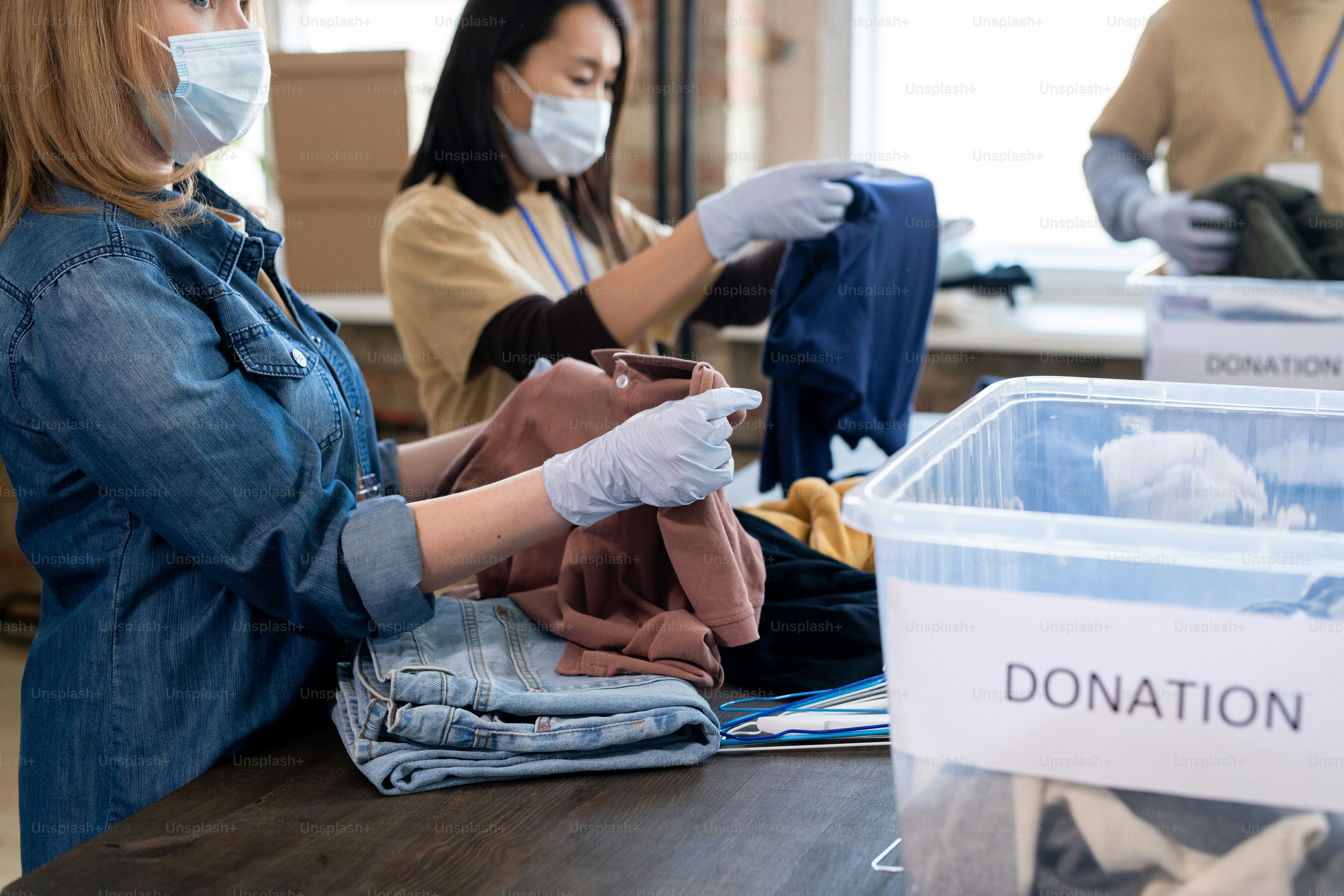 Young woman in gloves and mask unfolding t-shirt over table photo ...