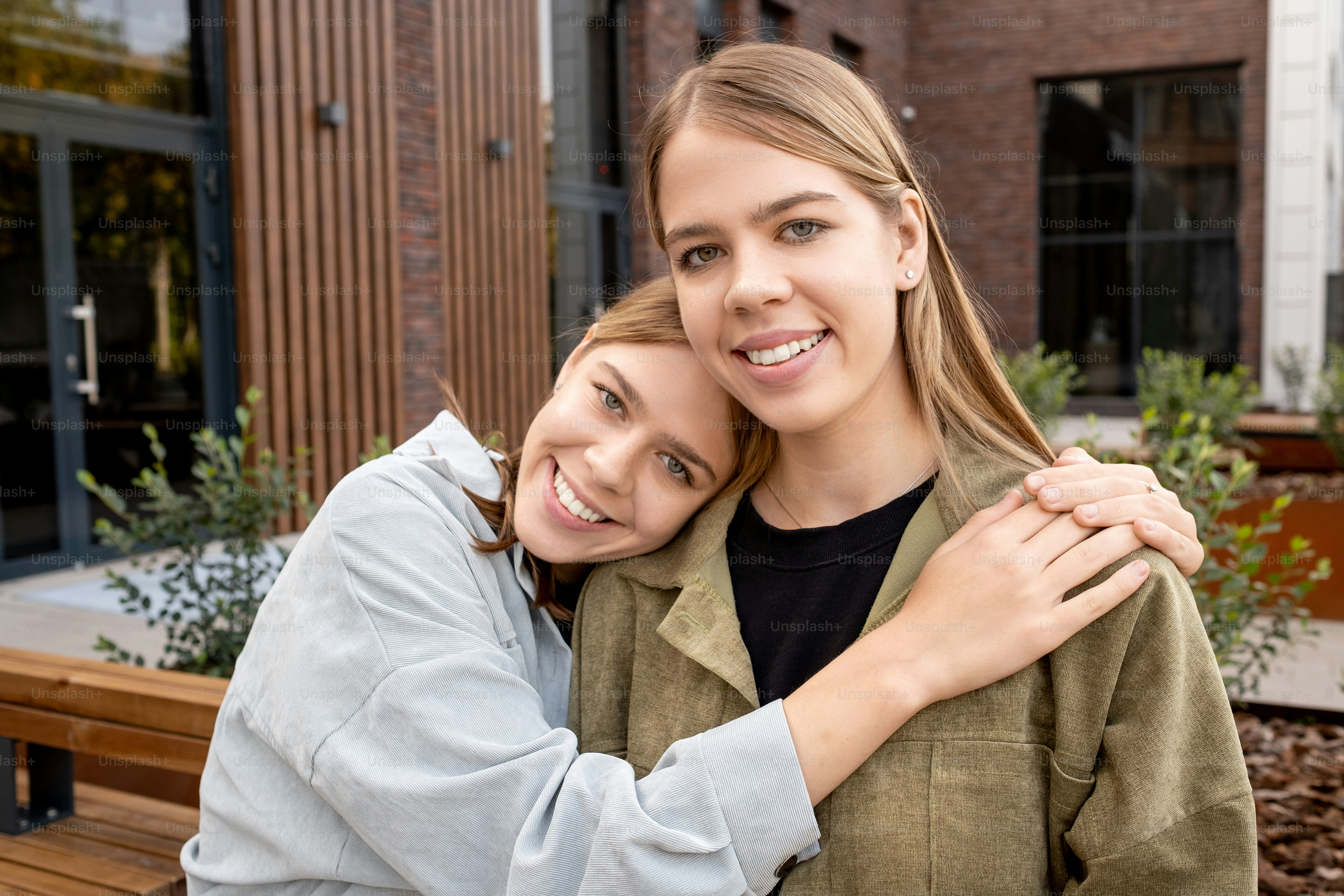 Affectionate twin girls in t-shirts and jackets looking at camera while ...