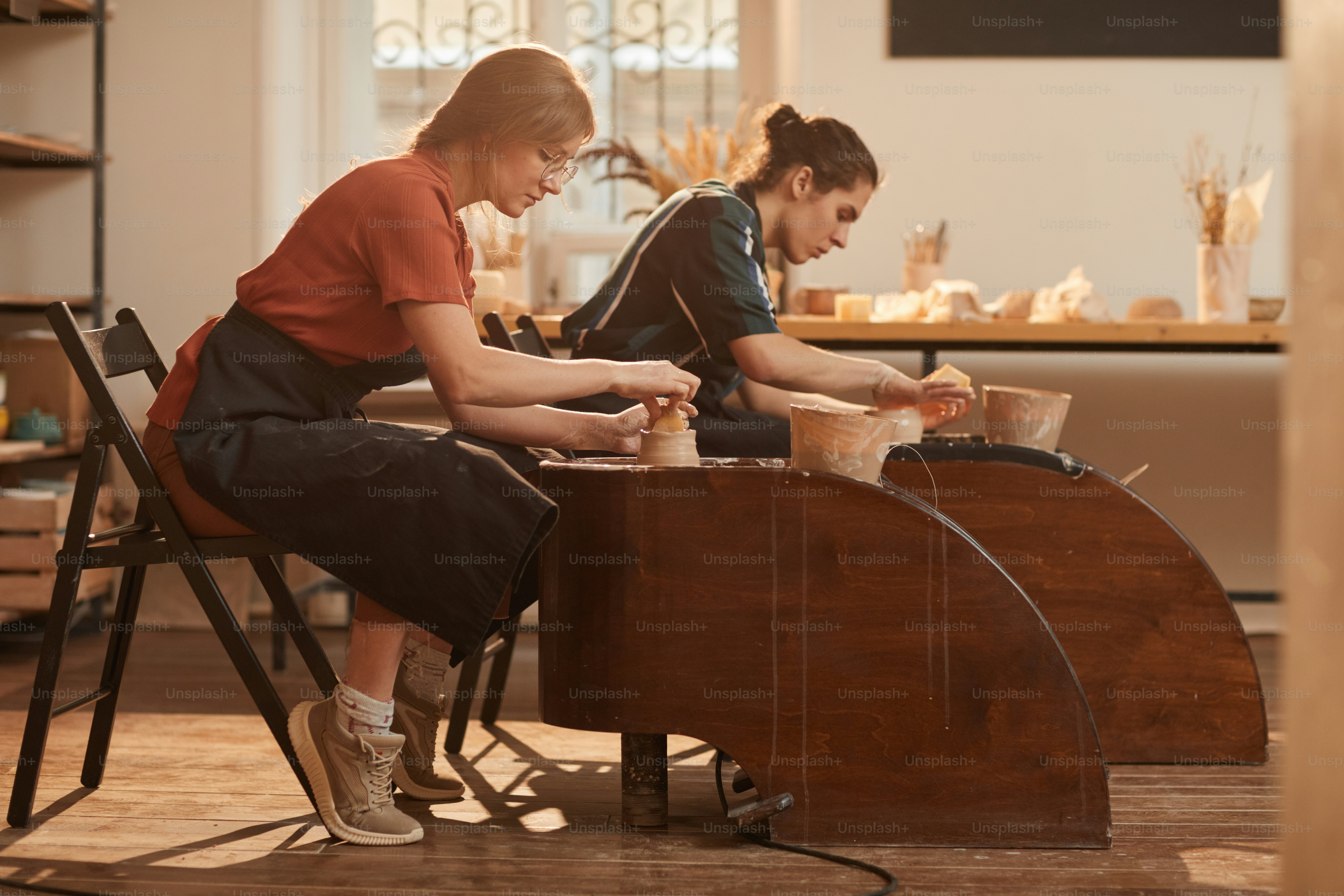 Full length side view portrait of two young people shaping clay on ...
