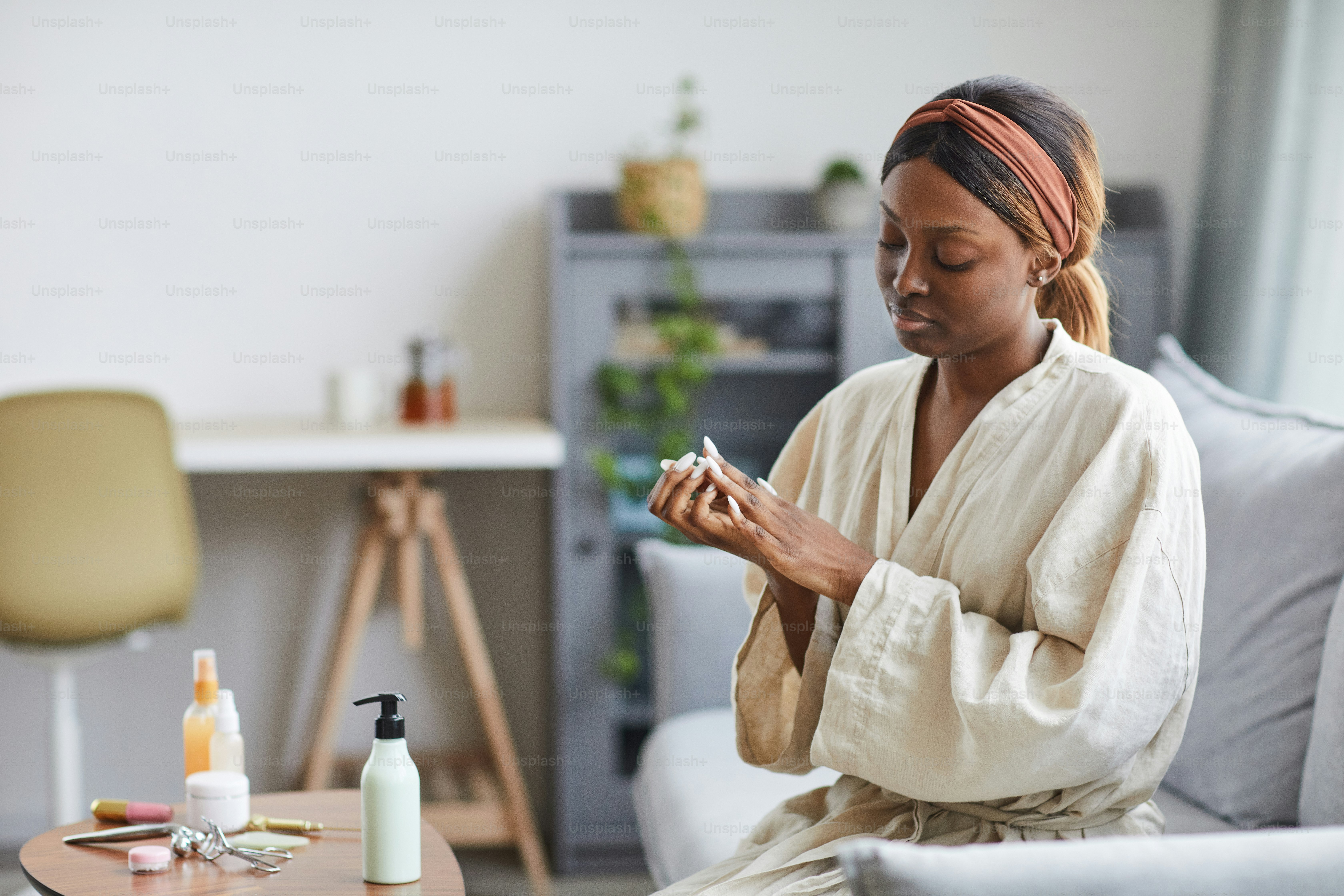 Minimal portrait of young African-American woman using face cream or ...