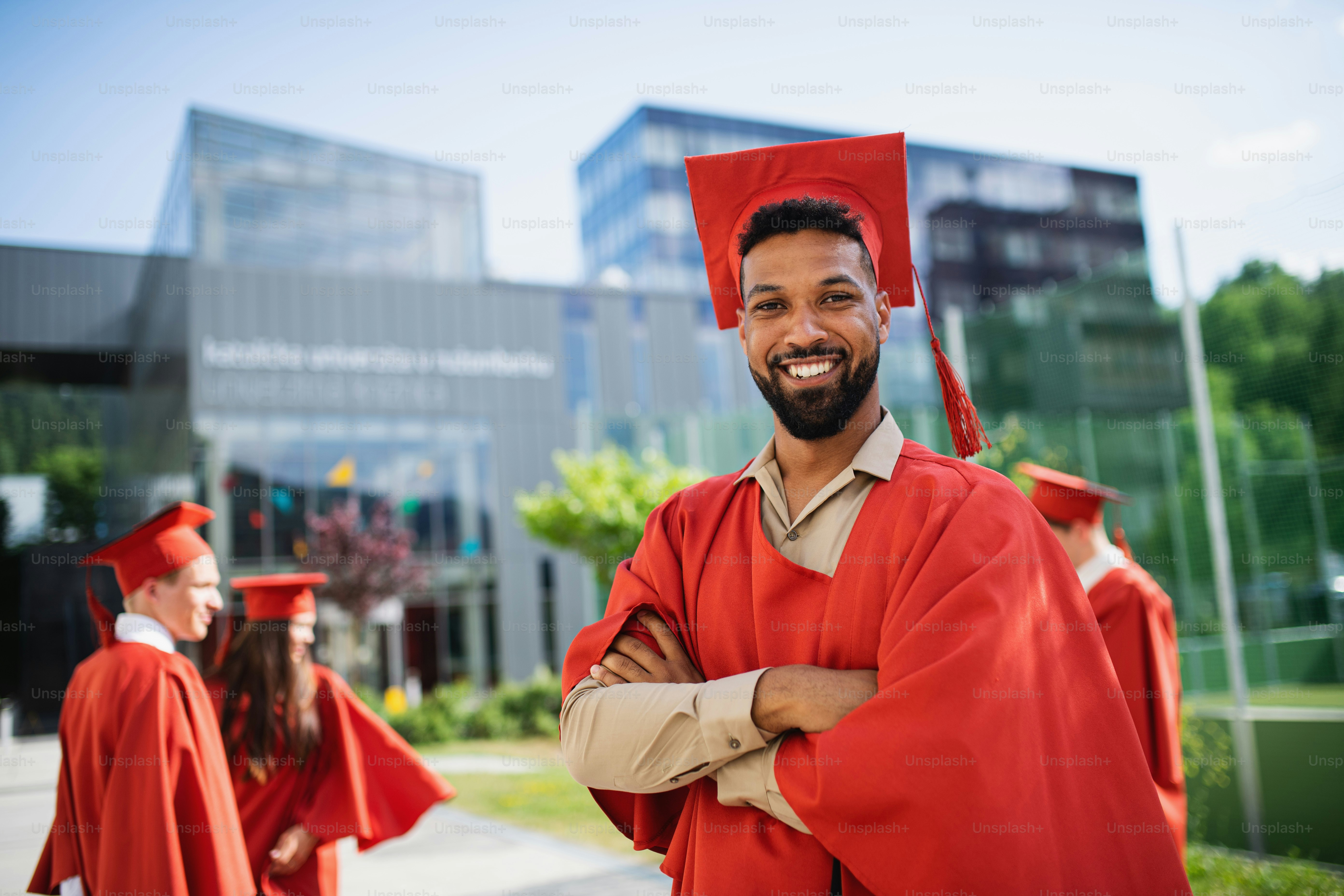 Portrait of happy university student with hat and gown looking at ...
