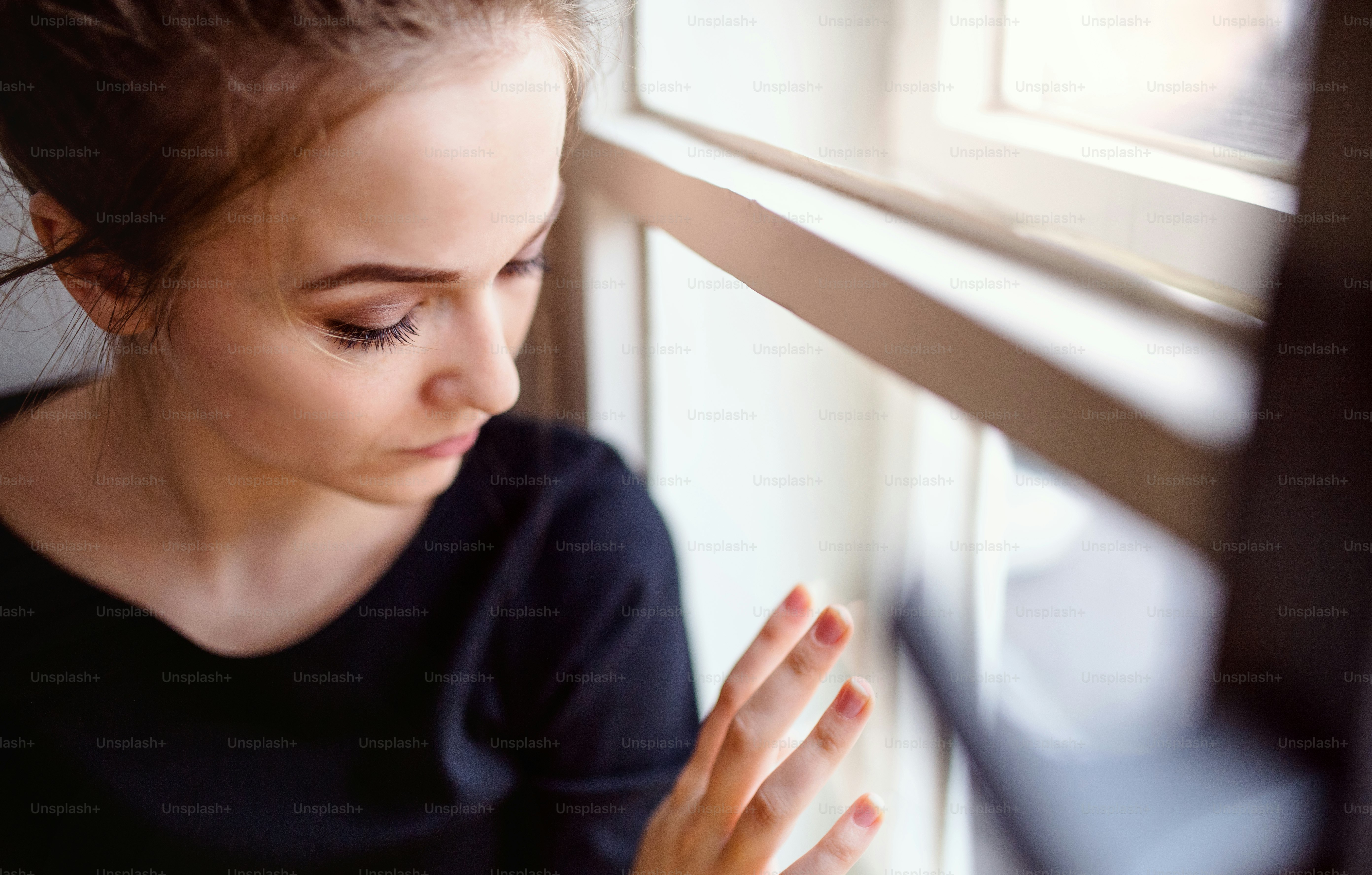 A close-up of young sad and frustrated female student sitting on window ...