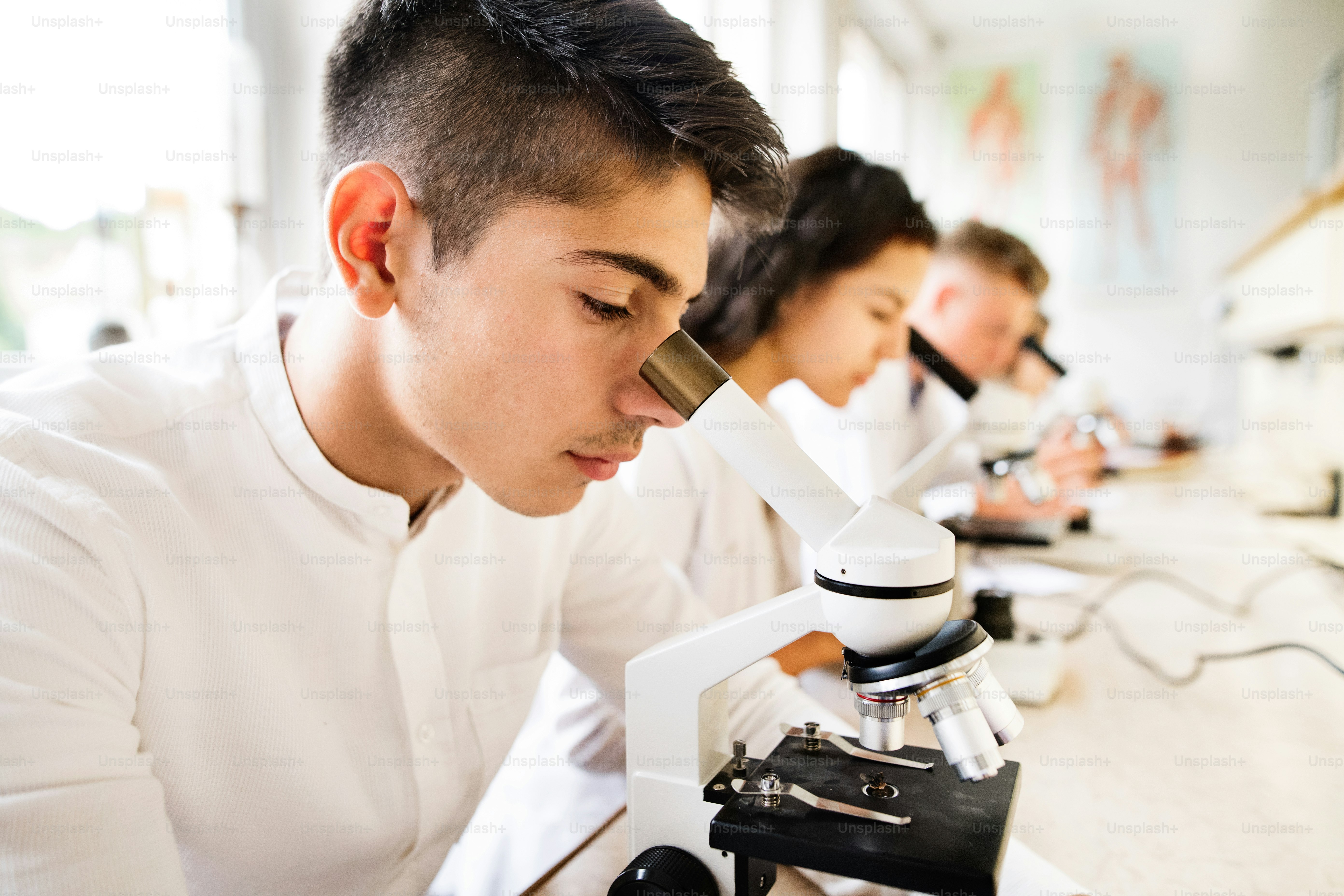 Beautiful high school students with microscopes in laboratory during ...