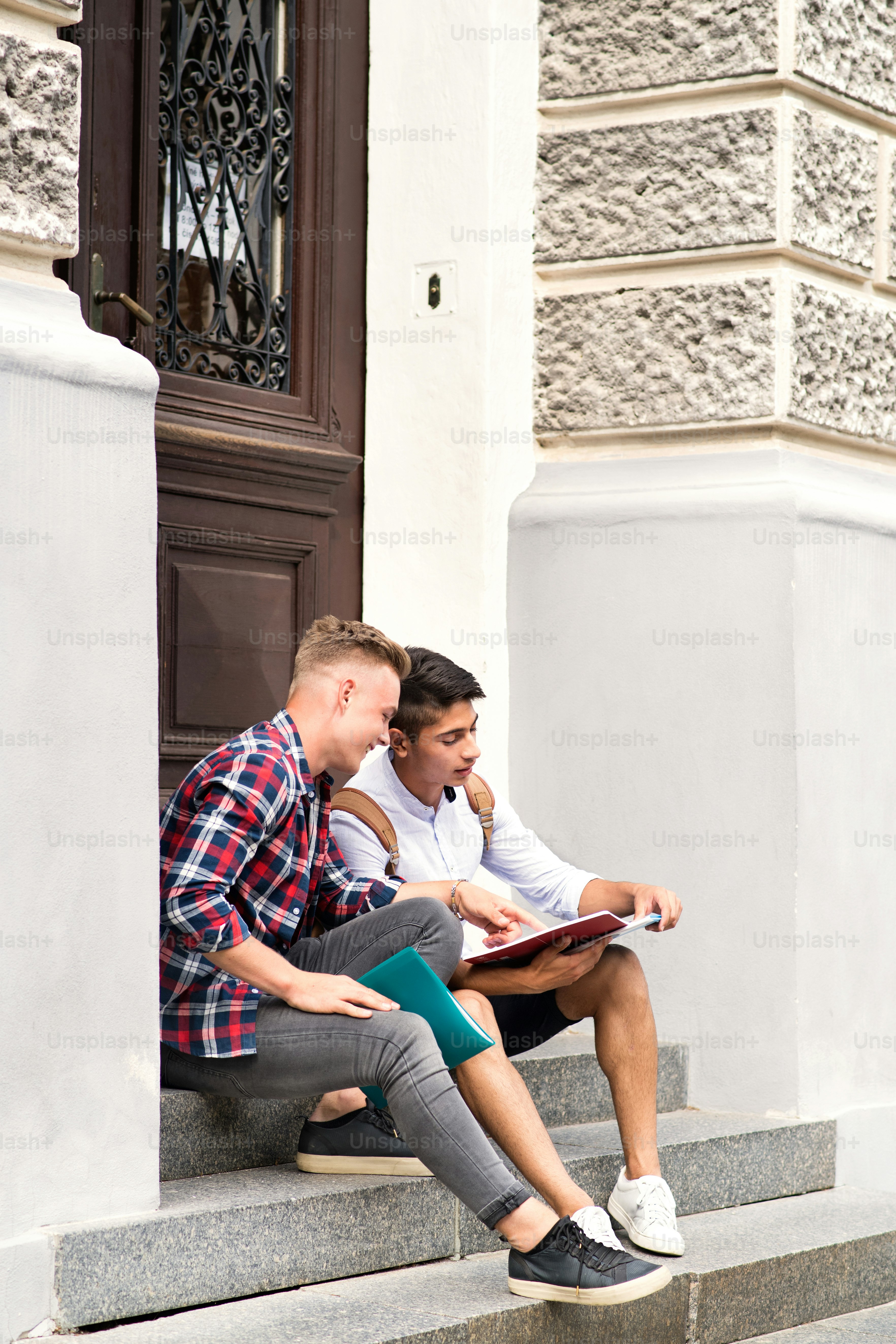 Two handsome teenage students sitting on stone steps in front of ...