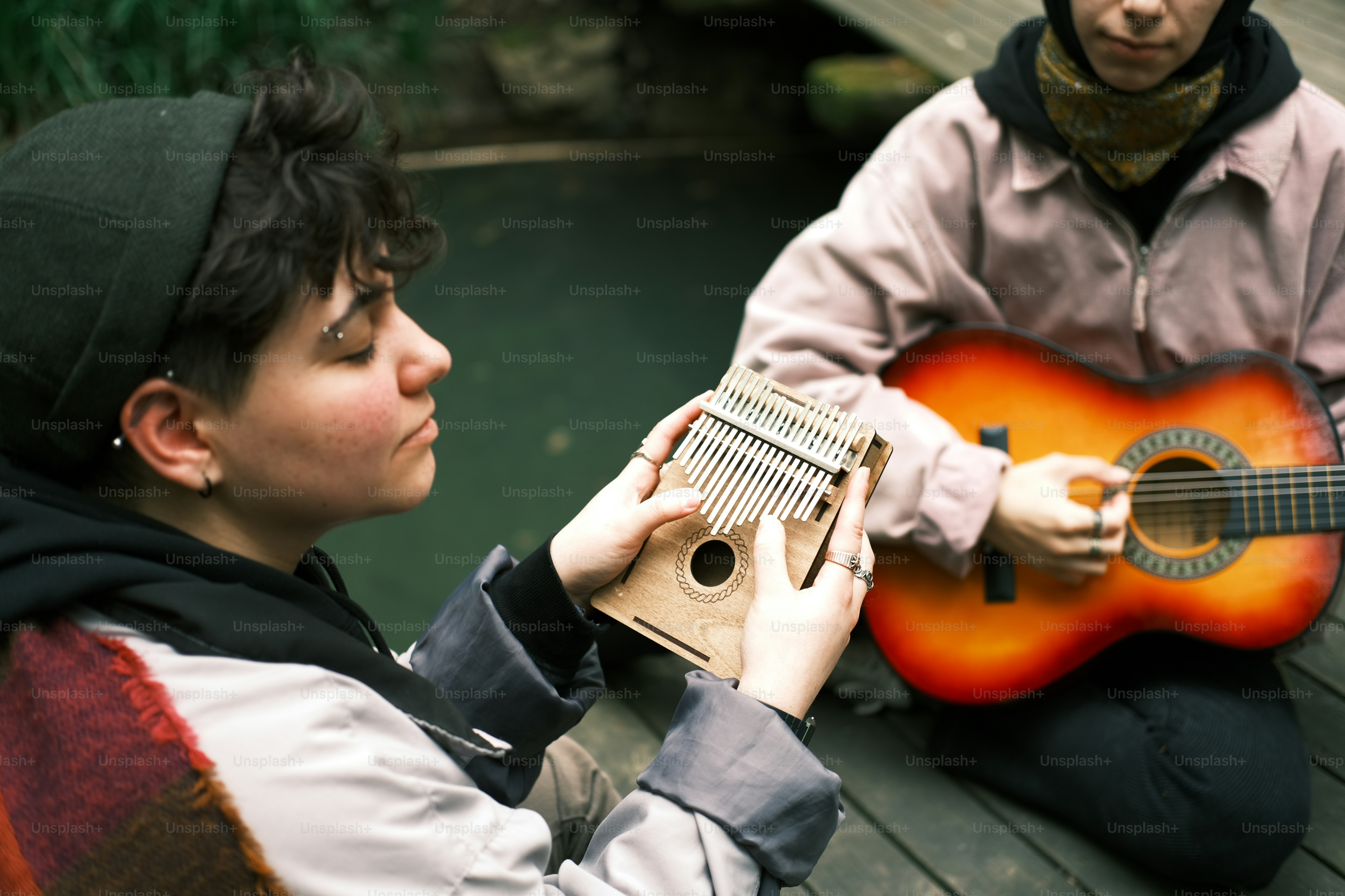 Two people sitting on a dock playing a musical instrument photo ...