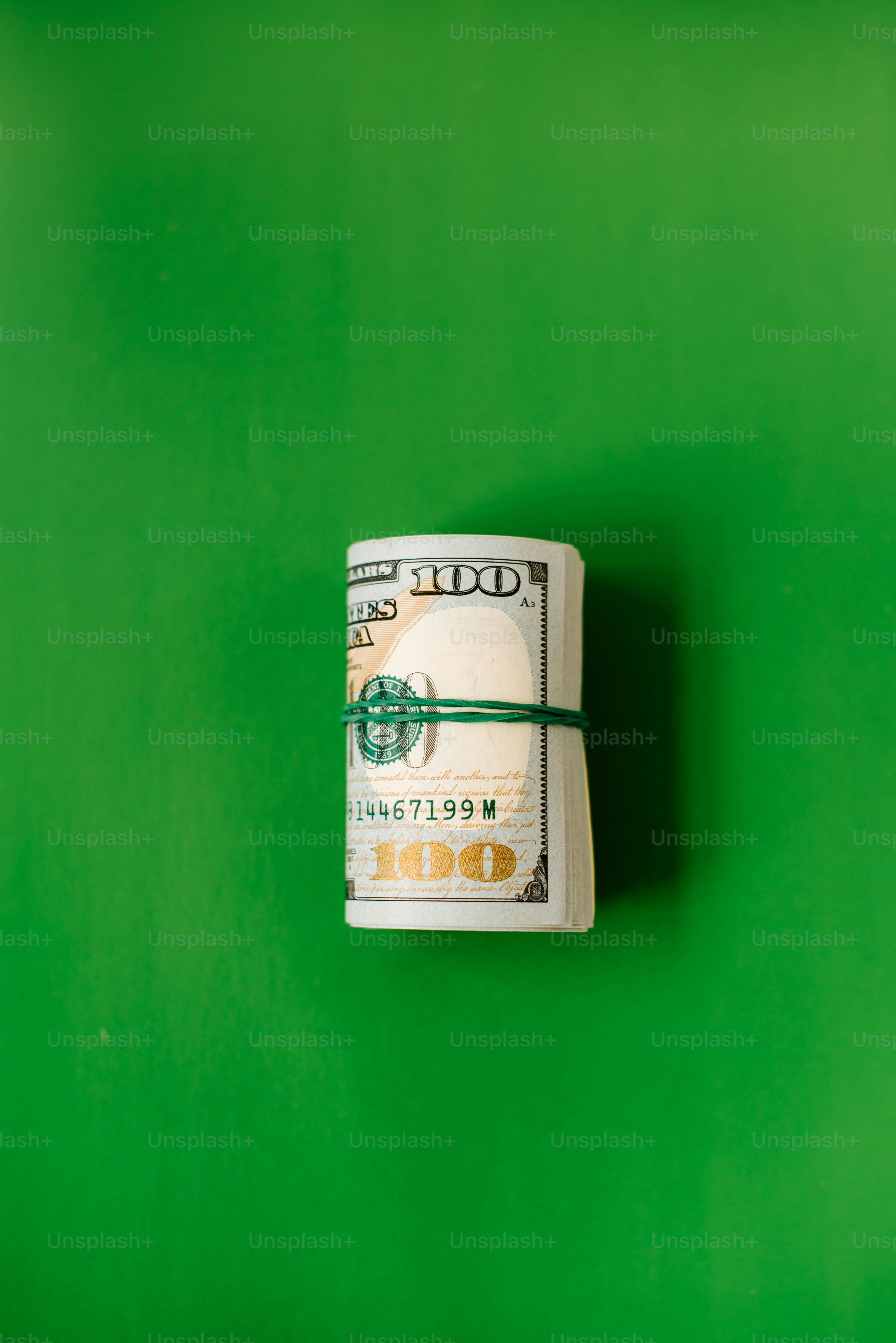 A roll of one hundred dollar bills wrapped in a green string photo ...
