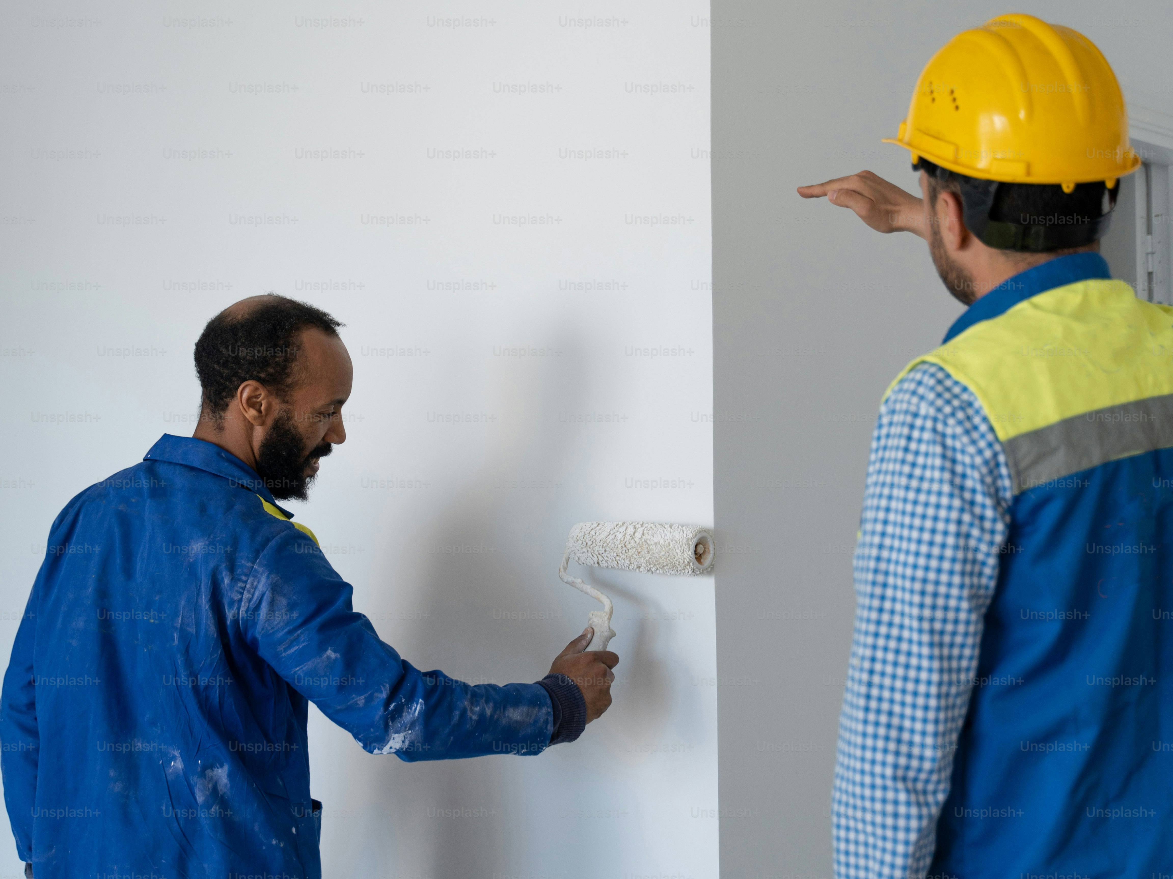 A man is painting a wall with a paint roller photo – Painting Image on ...