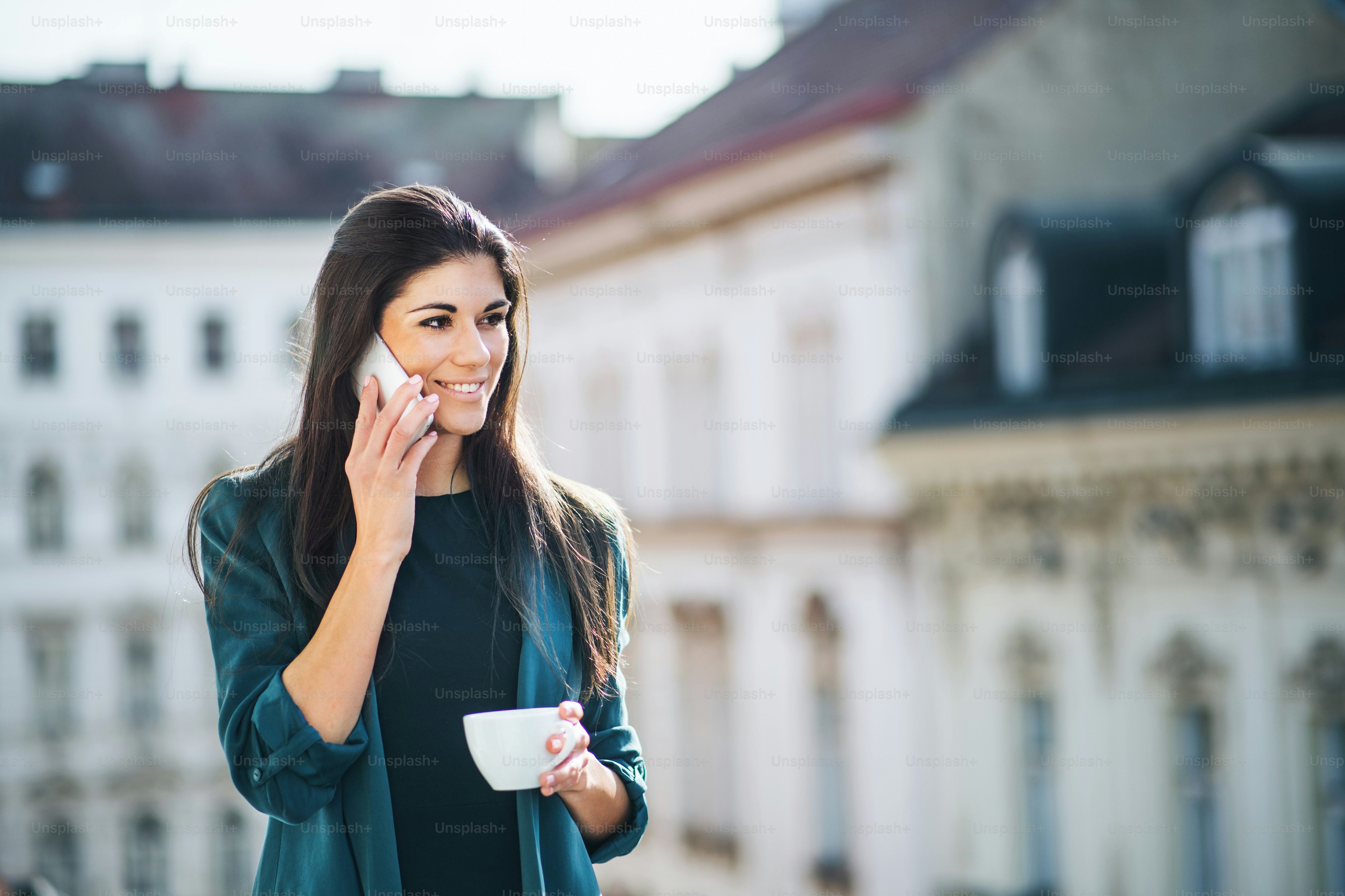 Young businesswoman with coffee and smartphone standing on a terrace ...