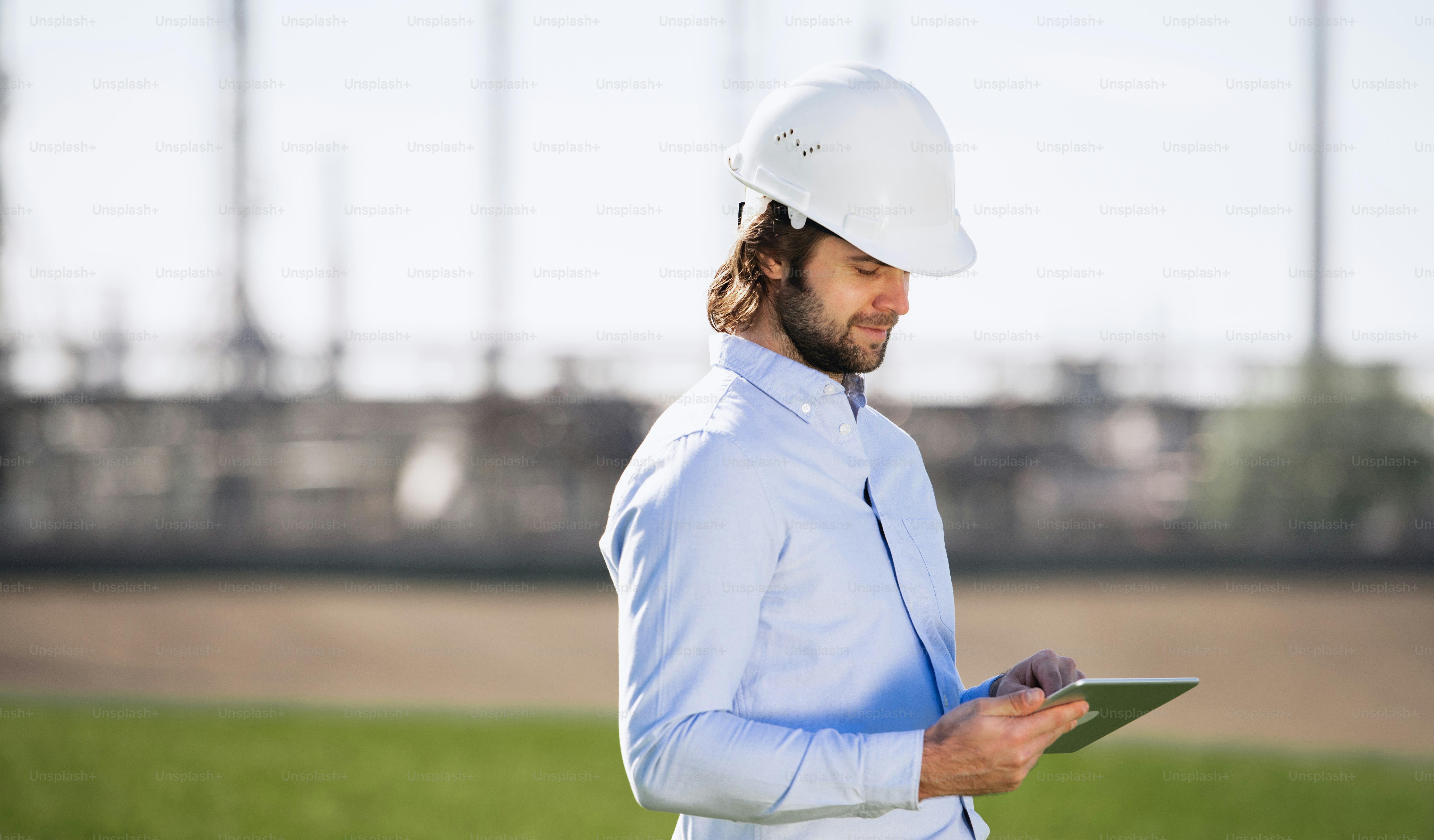Young engineer with hard hat and tablet standing outdoors by oil ...