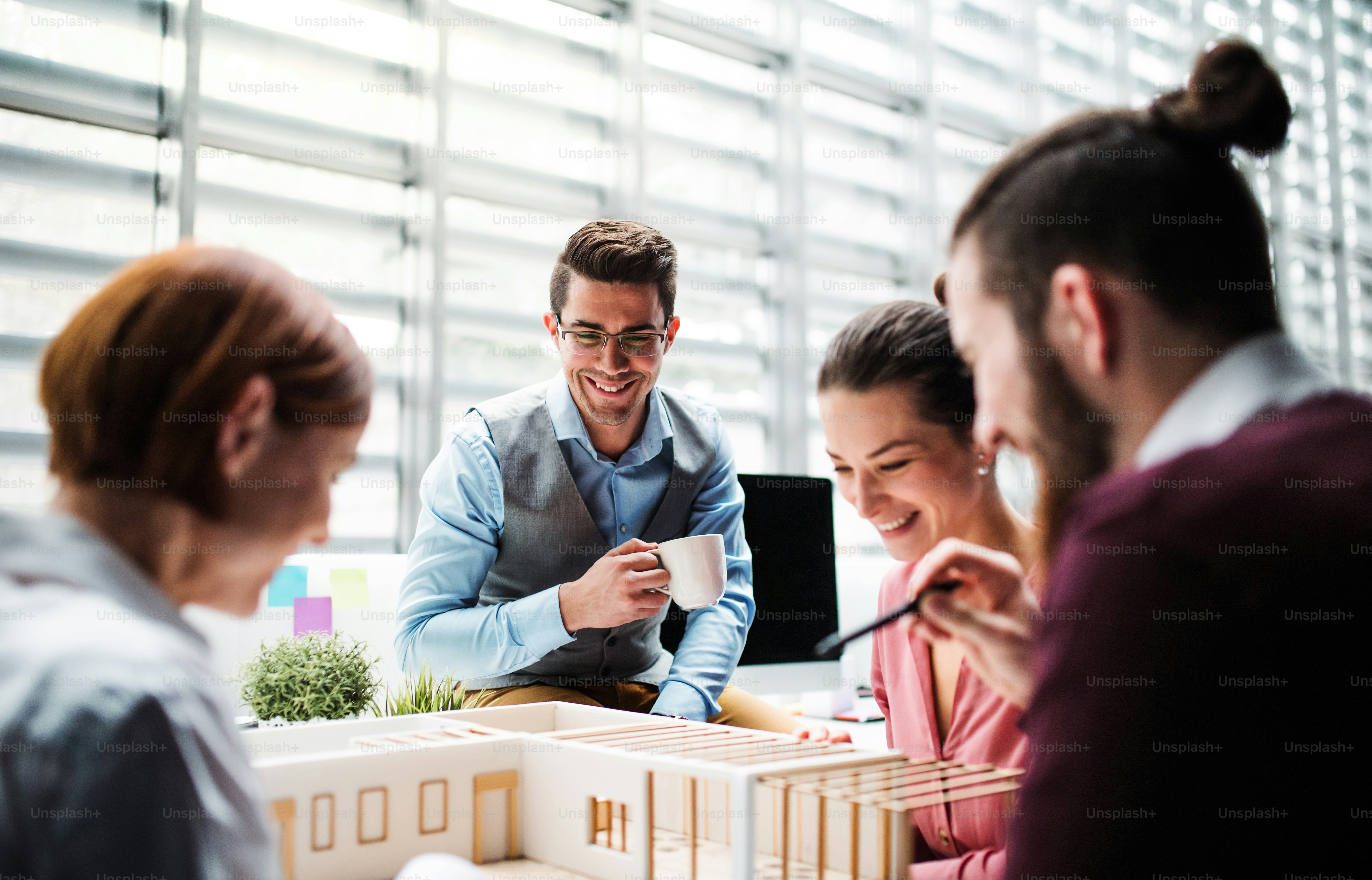 A group of young architects with model of a house standing in office ...