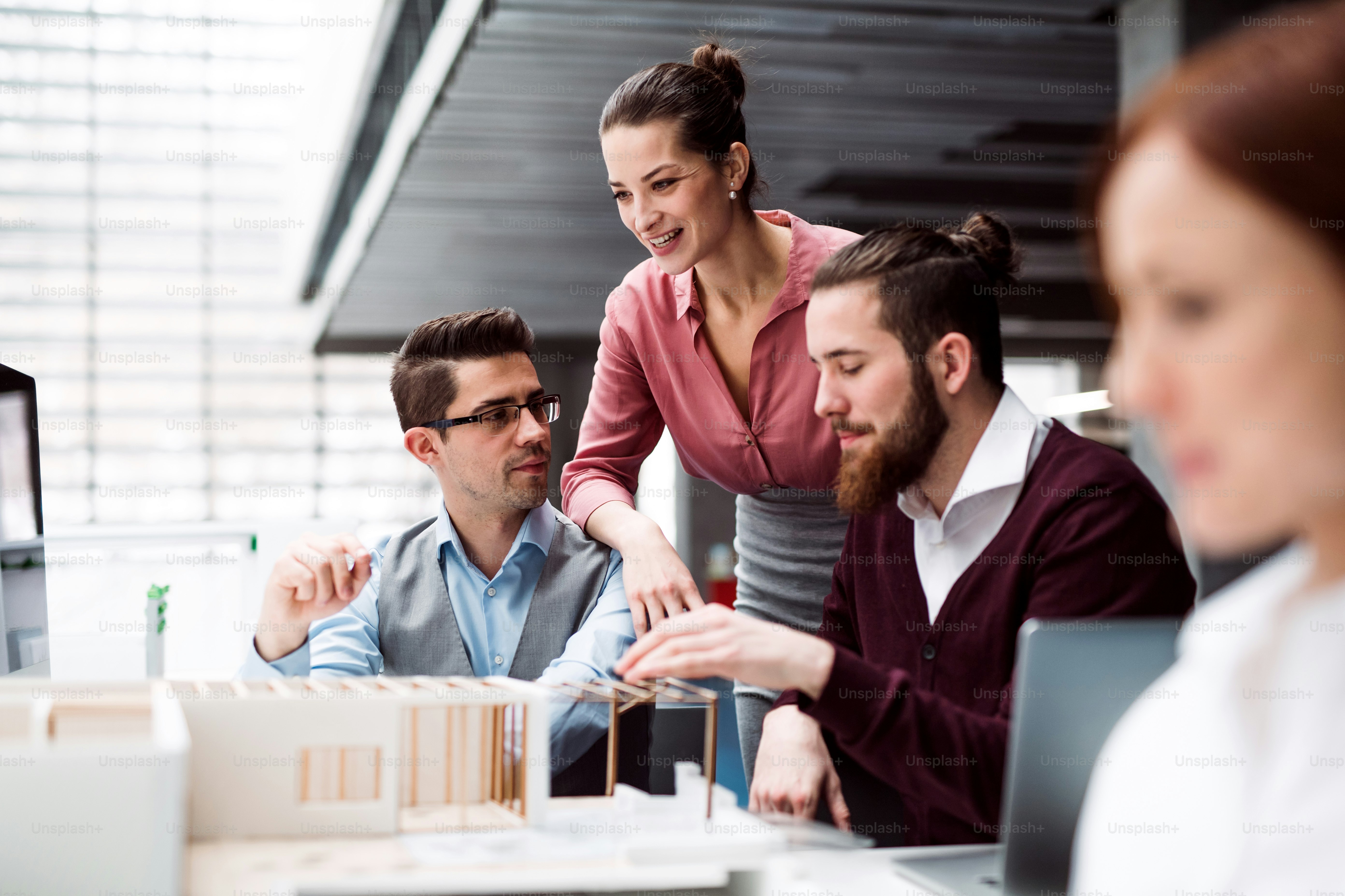 A group of young architects with model of a house working in office ...