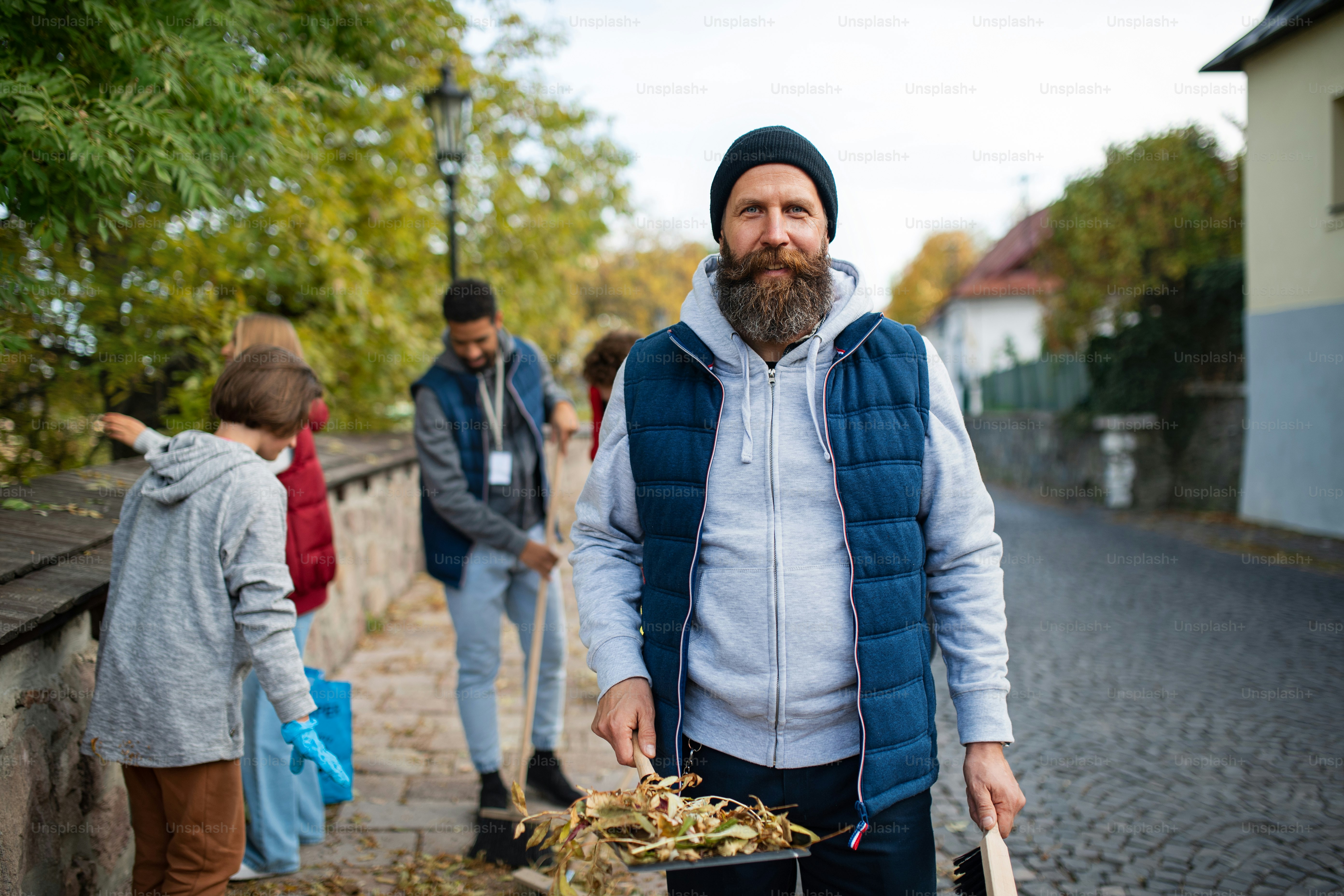 A mature man volunteer with team looking at camera and cleaning up ...
