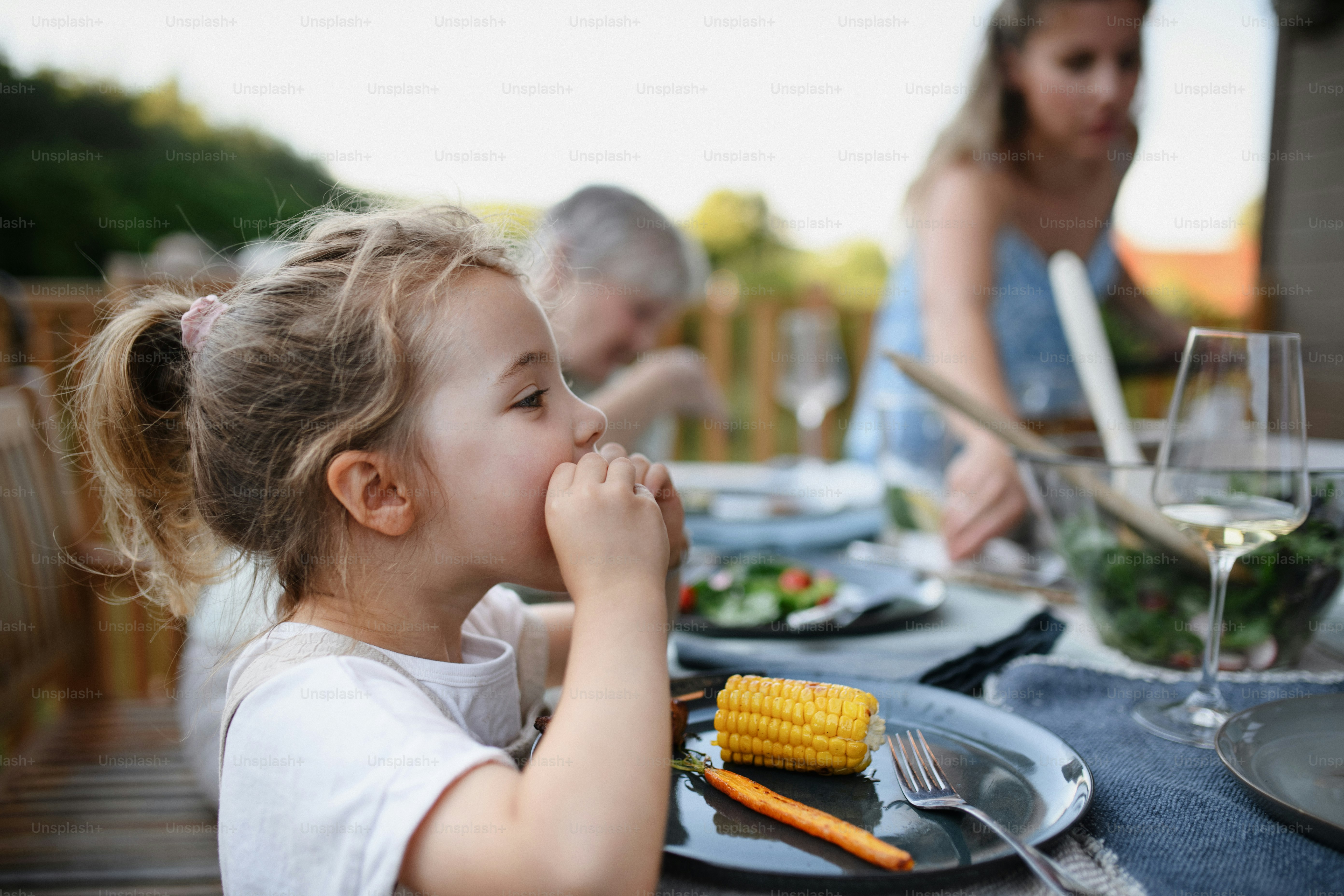 A family eating at barbecue party dinner on patio, little girl eating ...