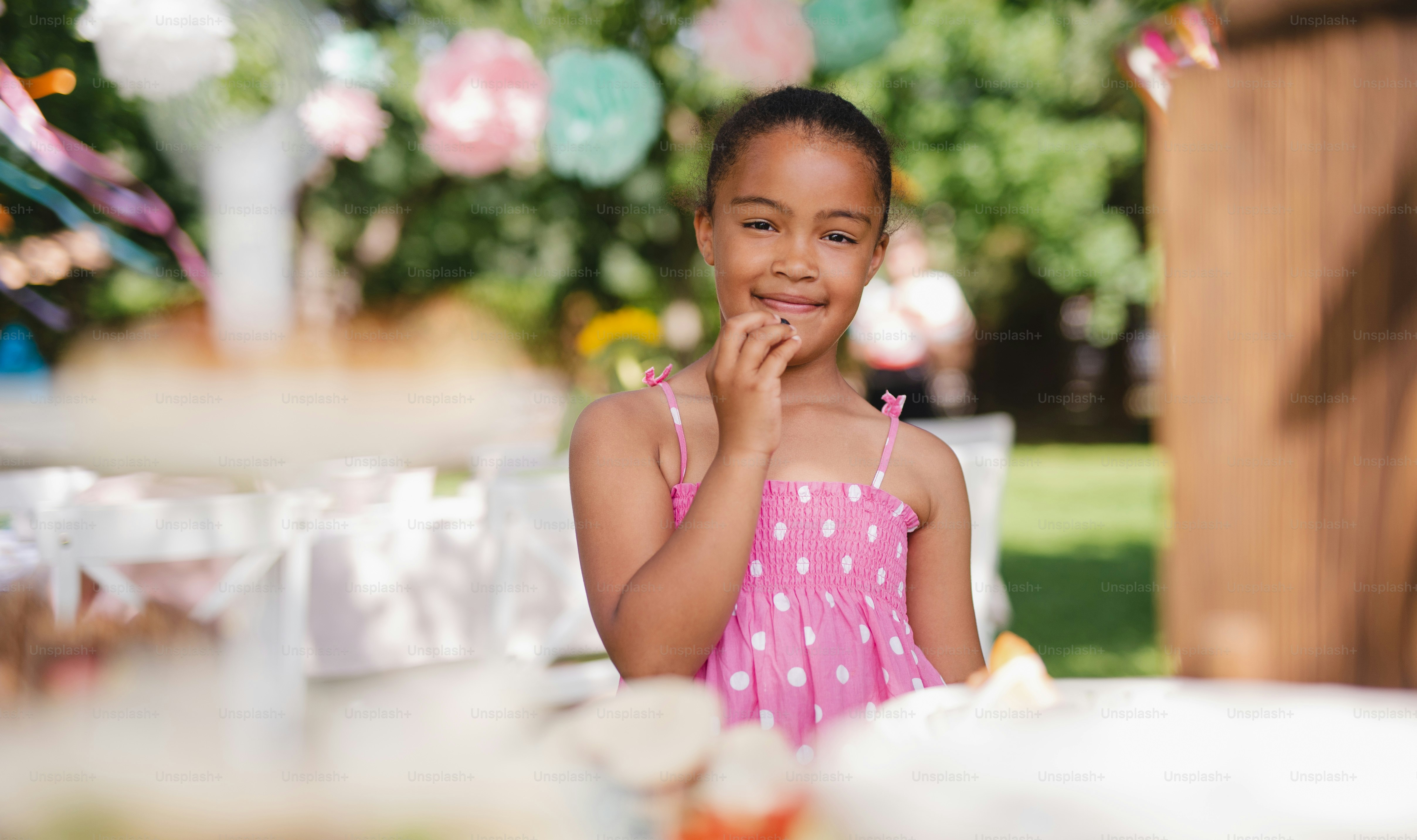 Small girl sitting outdoors in garden in summer, a birthday celebration ...